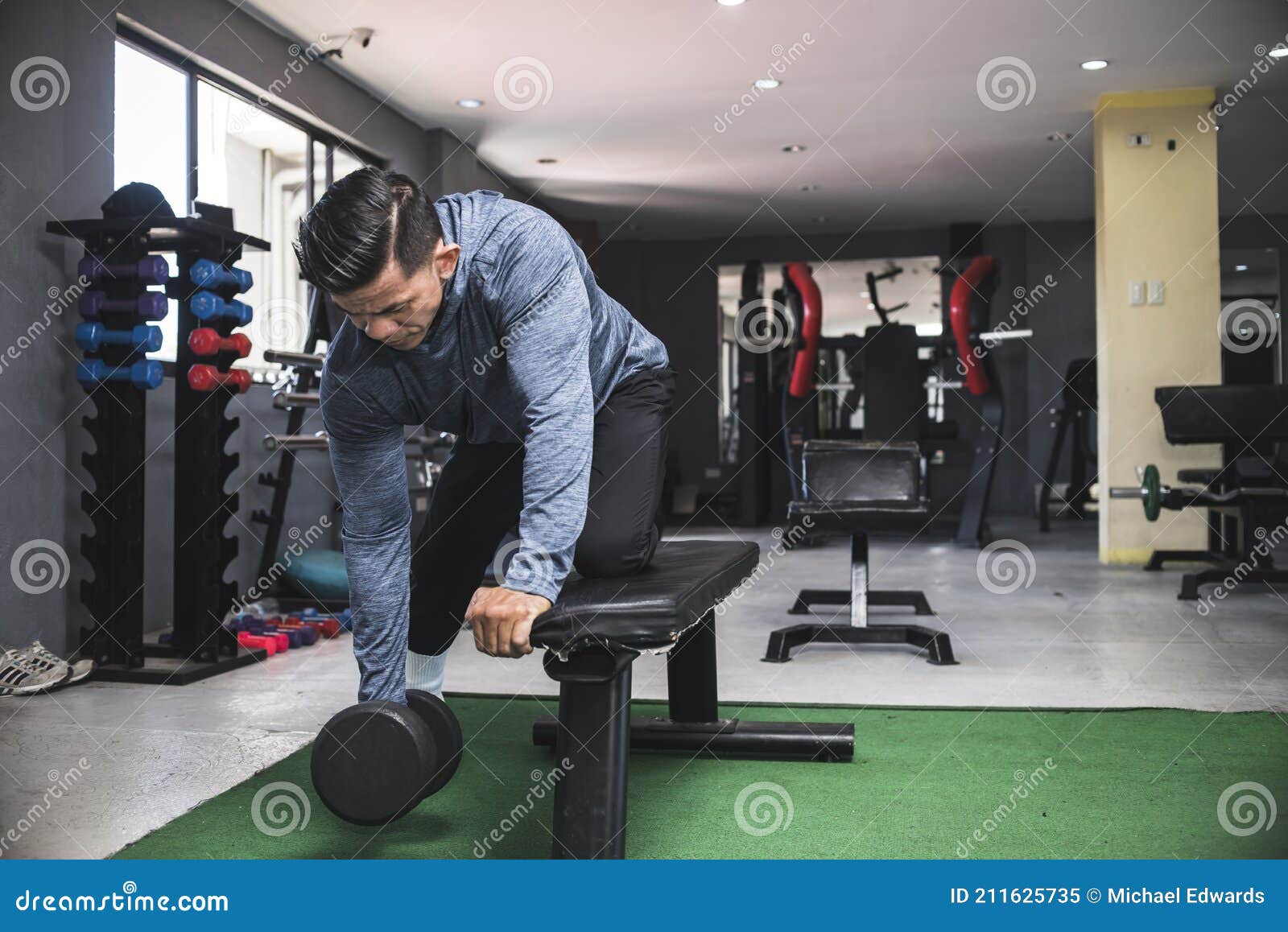 A Muscular and Buff Man in a Sweatshirt Does One Arm Dumbbell Rows ...