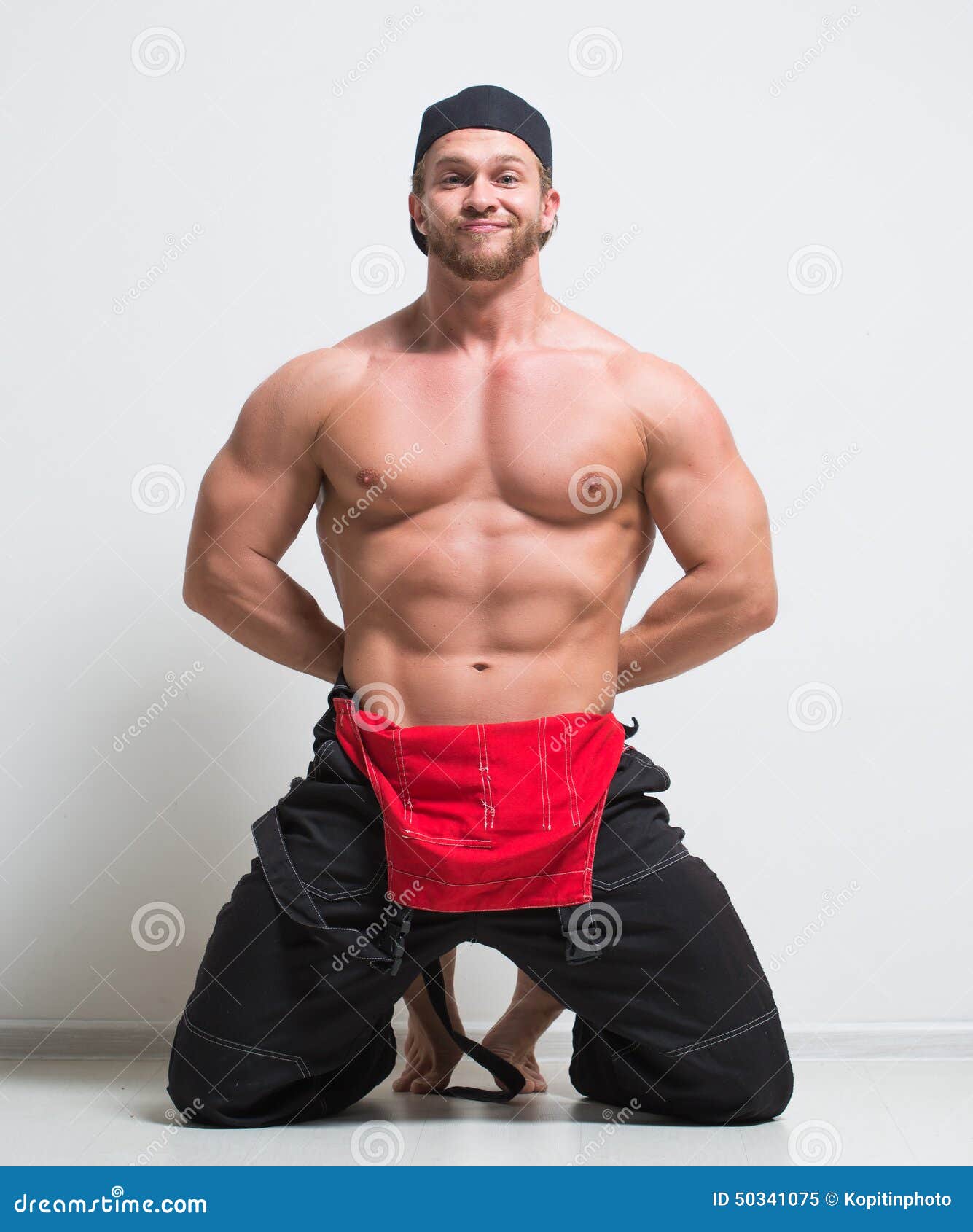 Muscular construction worker in overalls. kneeling
