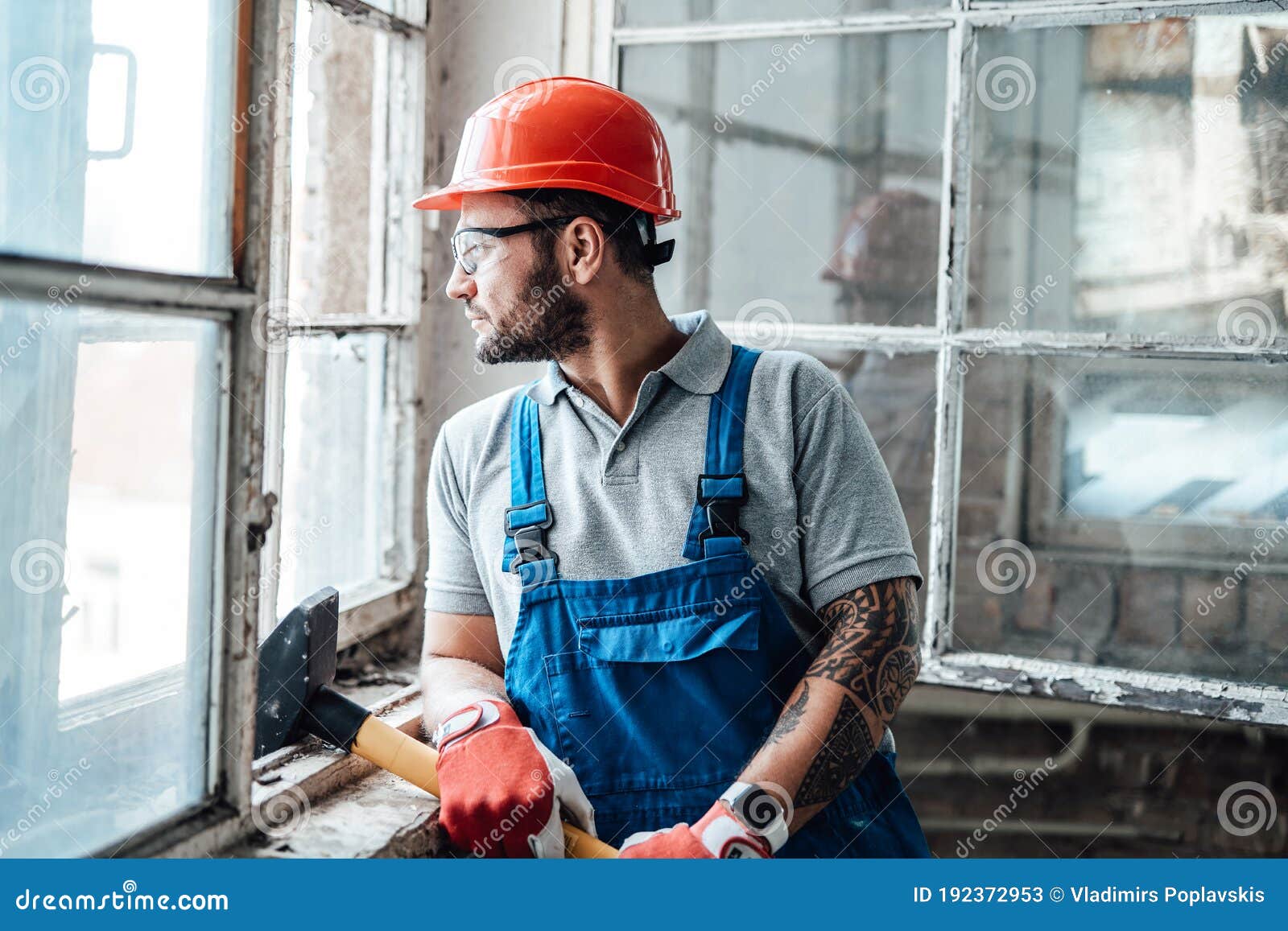 Muscular Construction Worker Stands by the Window and Holds a Big ...