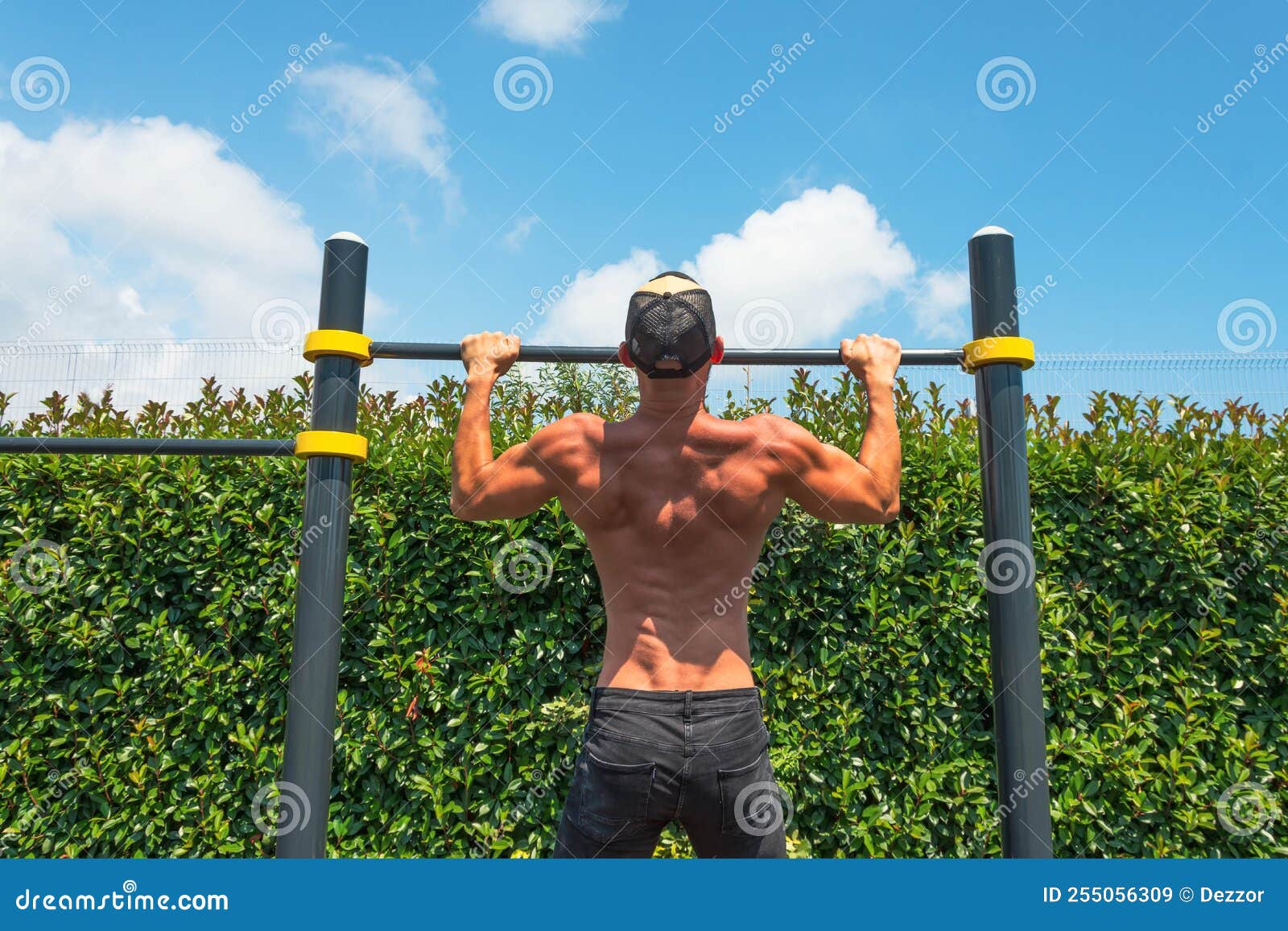 Muscular Man in a Cap Doing Pull-ups on the Horizontal Bar in the Park ...