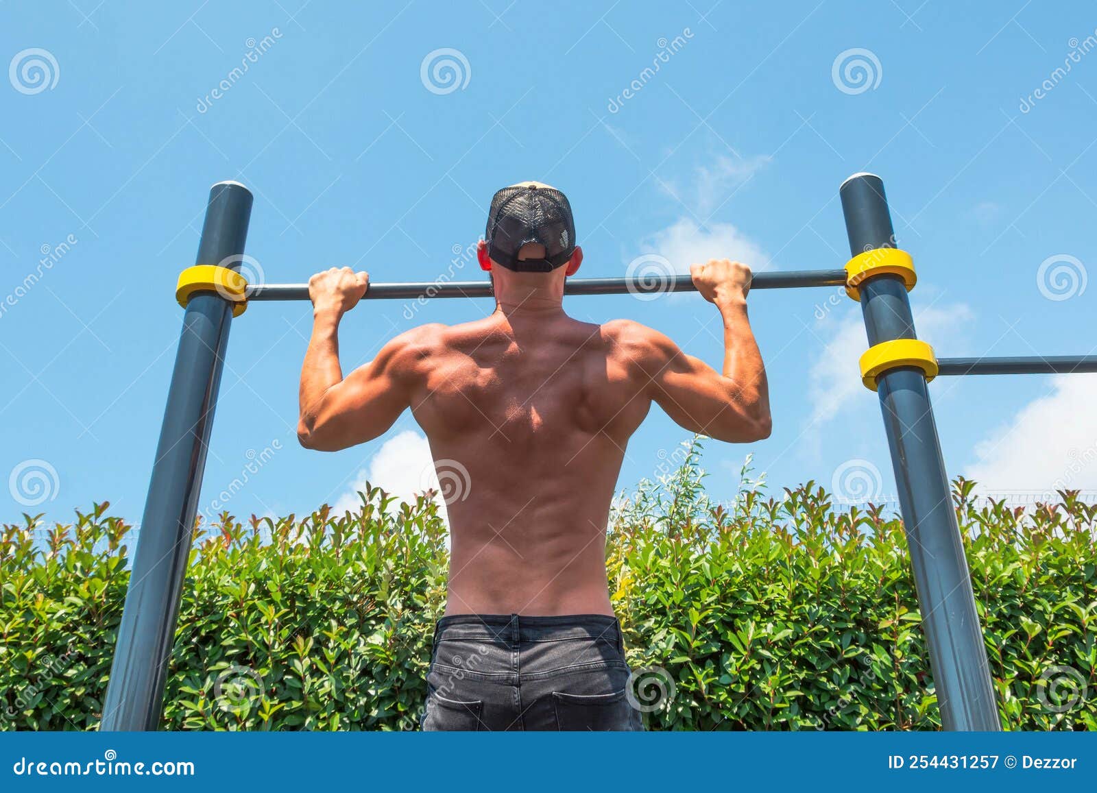 Muscular Man in a Cap Doing Pull-ups on the Horizontal Bar in the Park ...