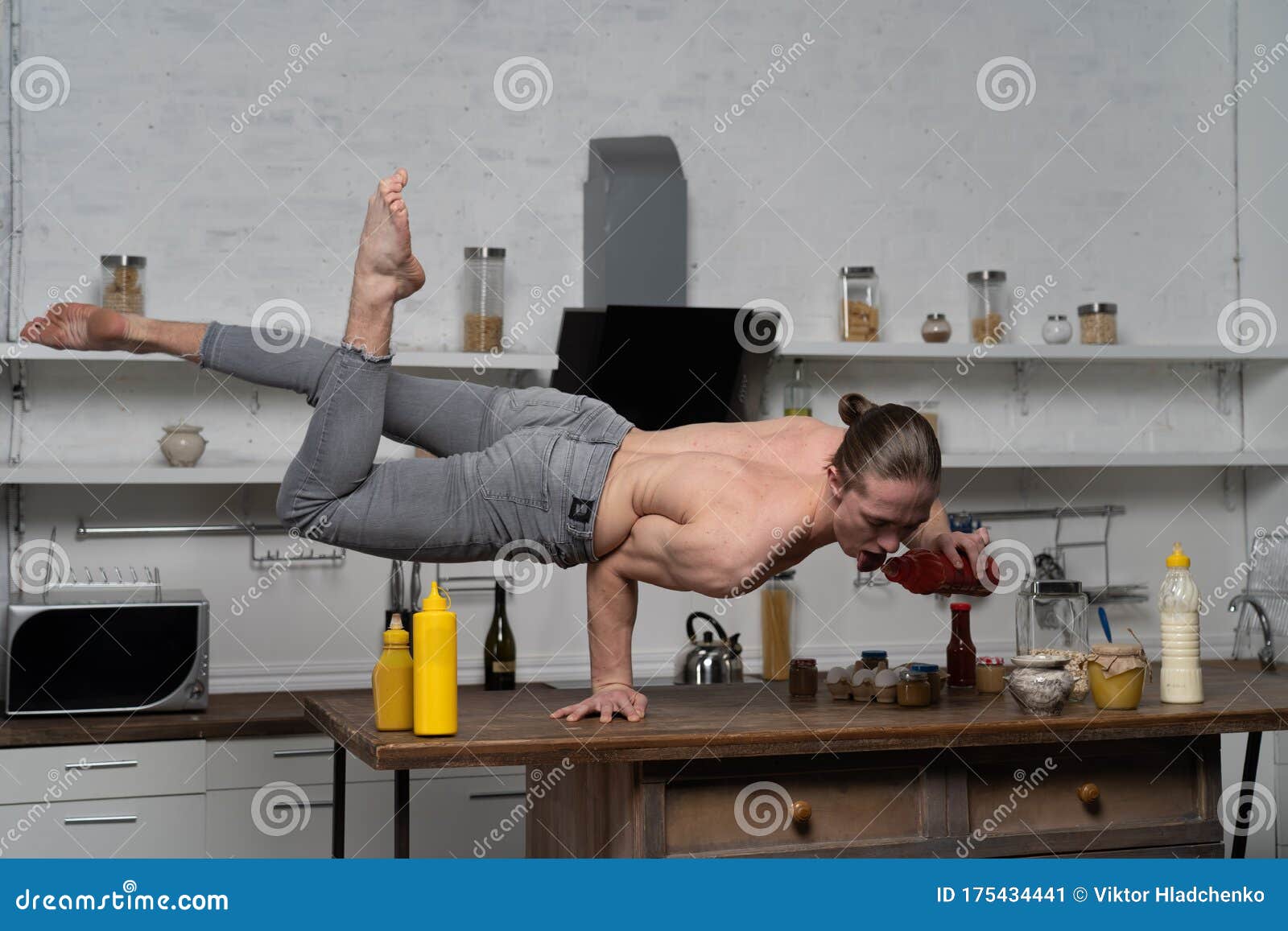 Muscular Man Stand on One the Hand in the Kitchen and Balancing Bottle ...