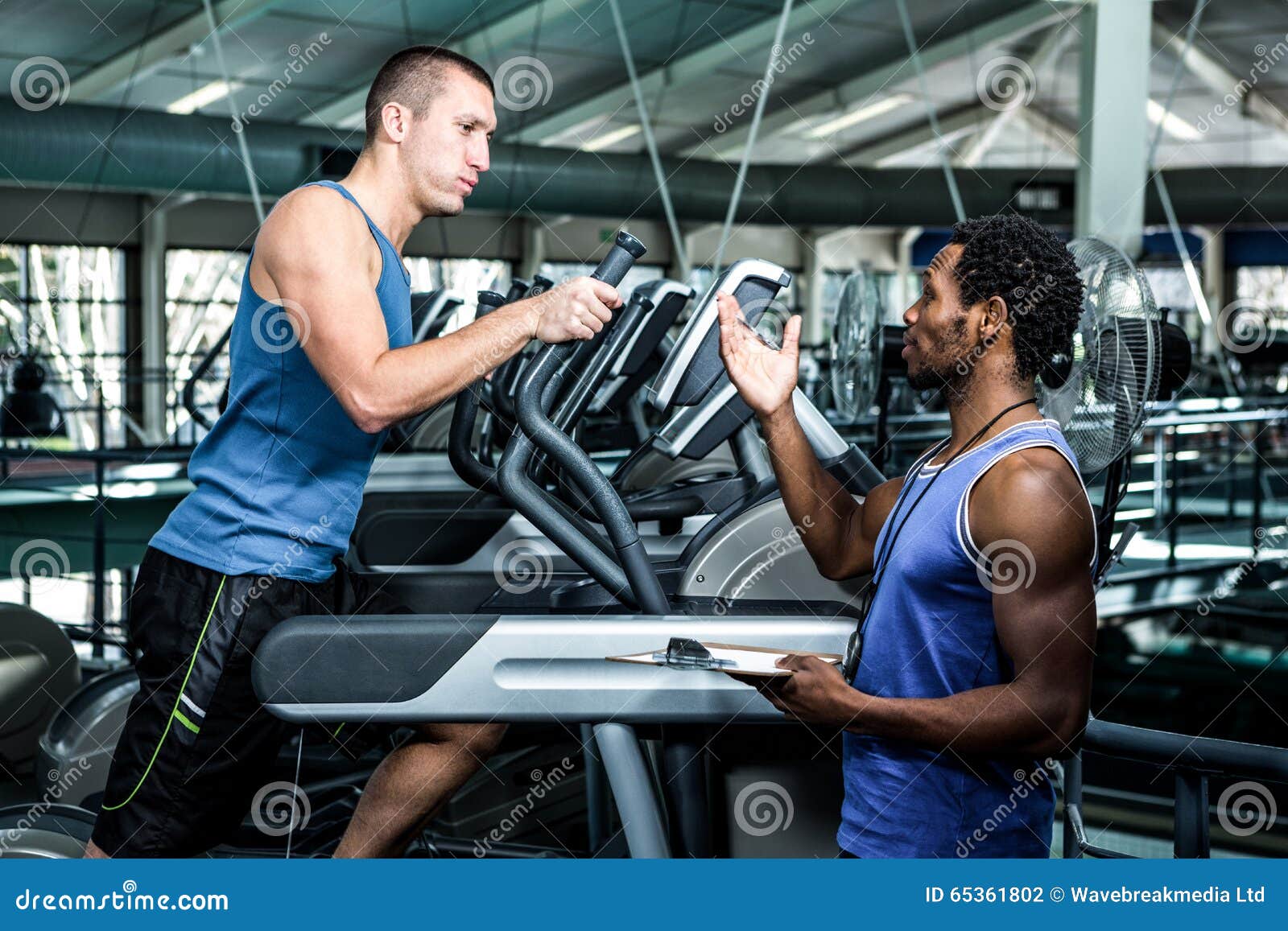 Muscular Man Using Elliptical Machine with Trainer Stock Photo - Image ...