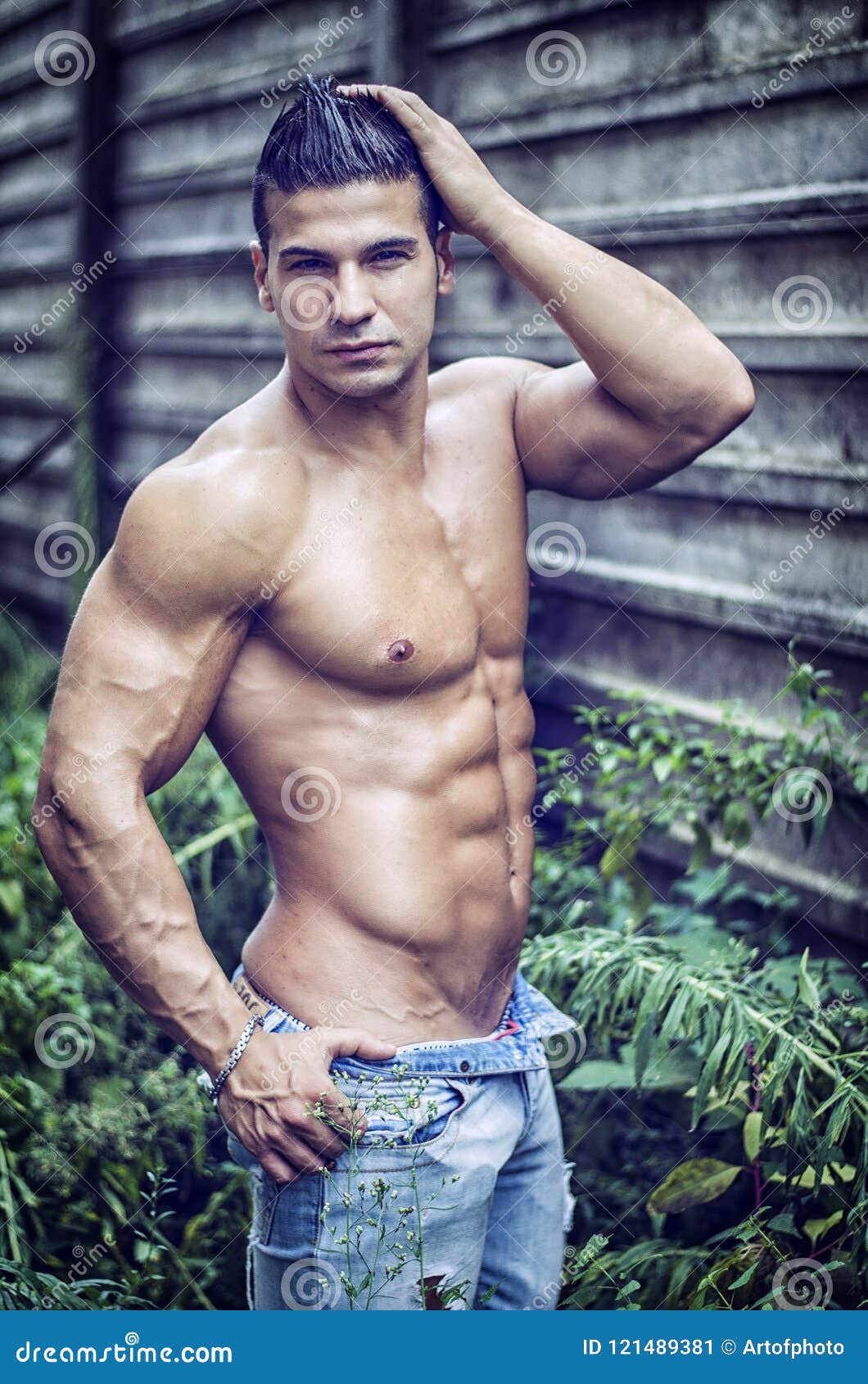 Muscular Young Latino Man Shirtless In Jeans In Front Of Concrete Wall