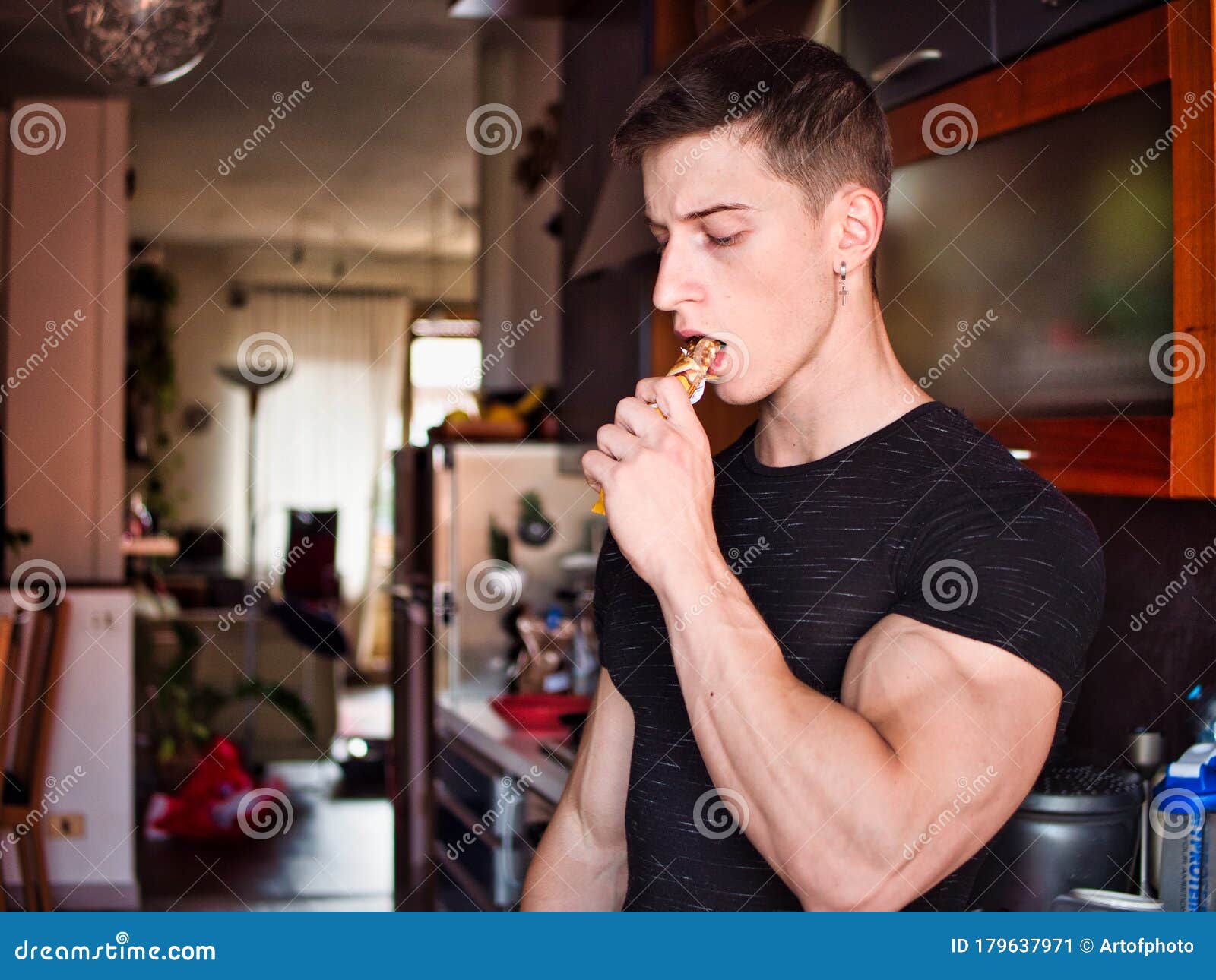 Muscular Young Man Eating Cereal Bar, Looking at Camera Standing, Stock ...