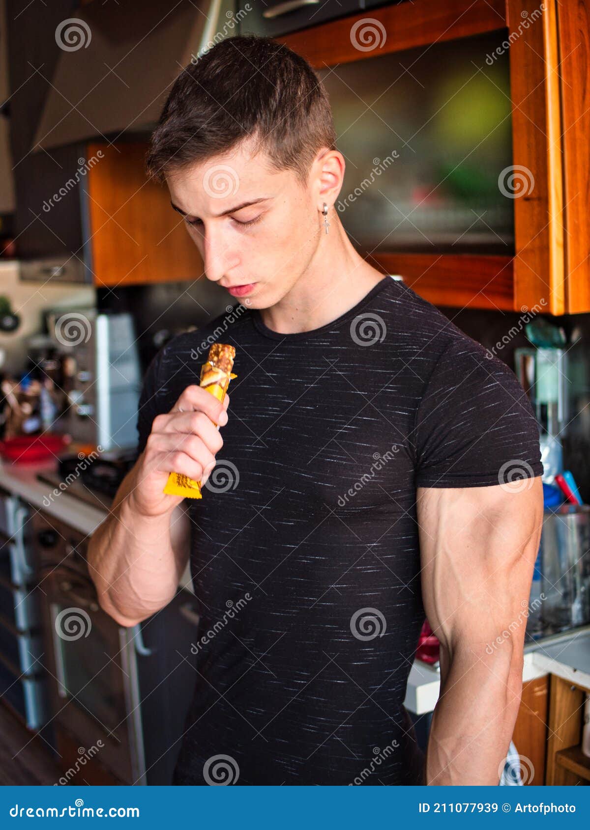 Muscular Young Man Eating Cereal Bar, Looking at Camera Standing, Stock ...