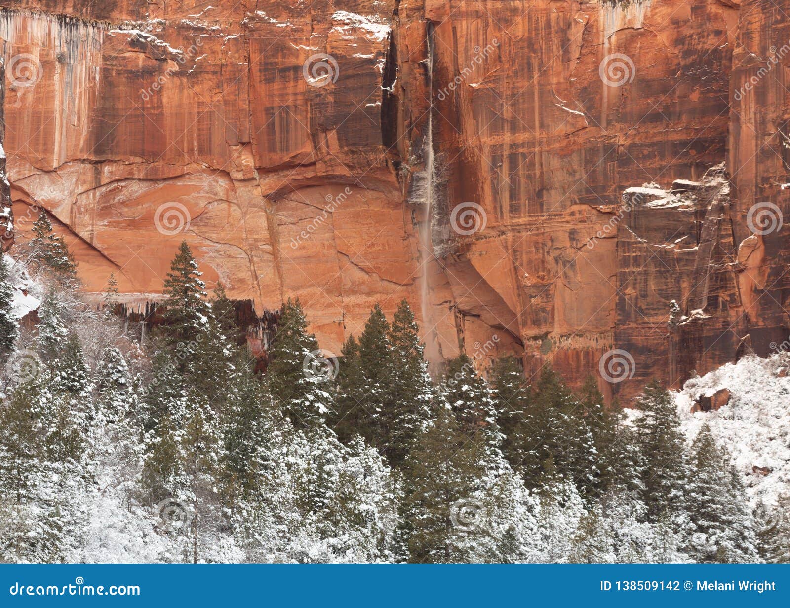 A Narrow Waterfall Streams Down a Red Sandstone Cliff Face in Front of ...