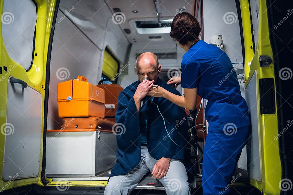 Nurse In Blue Medical Uniform Puts Oxygen Mask On Man Sitting In
