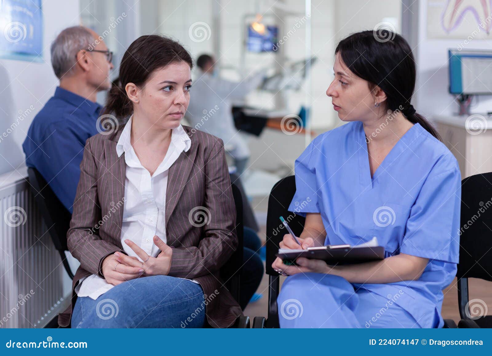 Nurse Taking Notes On Clipboard Discussing With Patient In Dental
