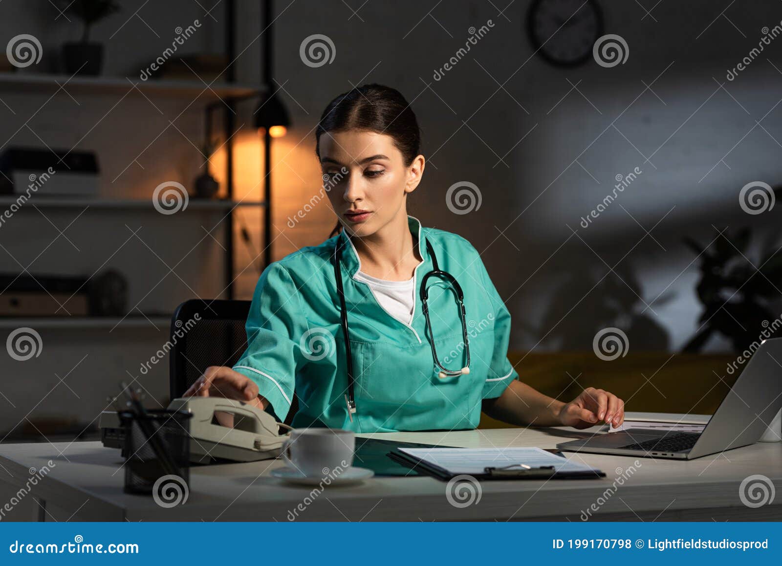 Nurse in Uniform Sitting at Table and Taking Handset during Night Shift ...