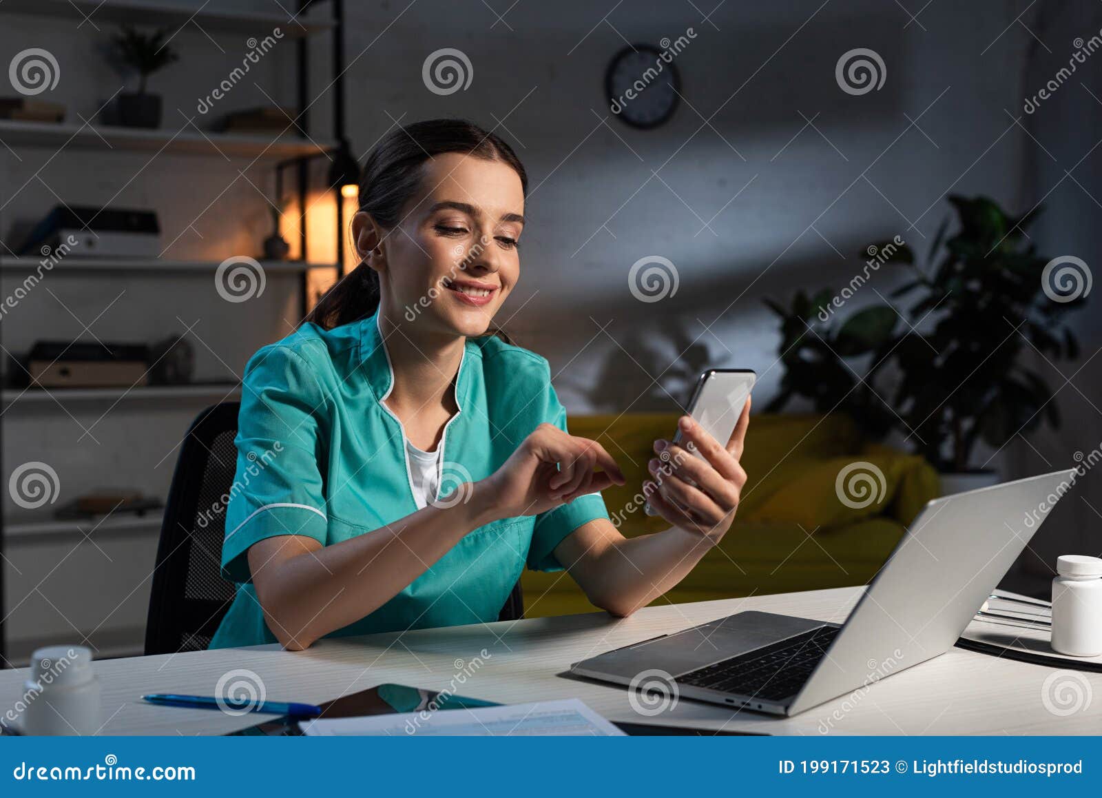 Nurse in Uniform Sitting at Table and Using Smartphone during Night ...