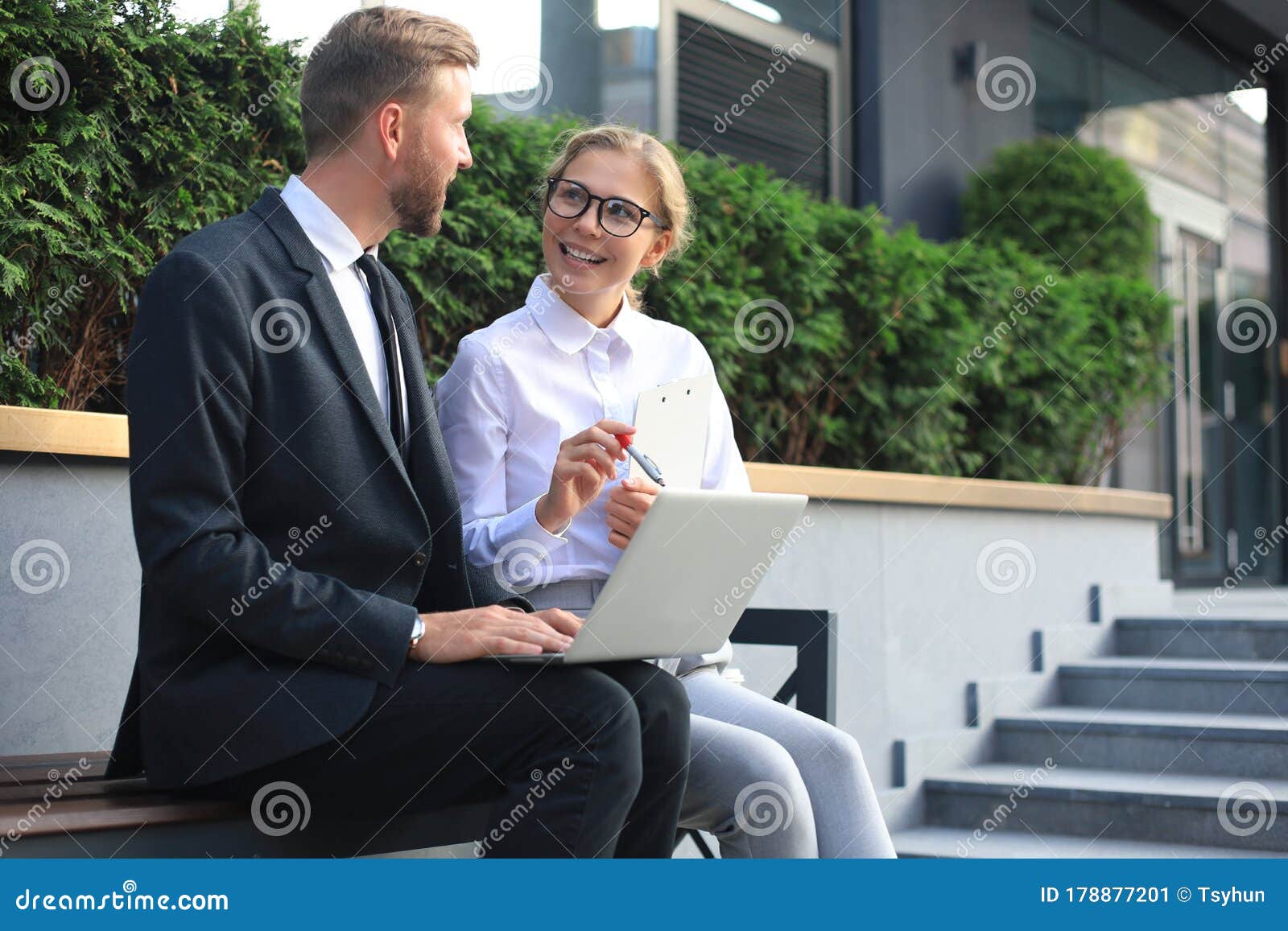 Office Colleagues Using Laptop Computer while Sitting on a Bench ...
