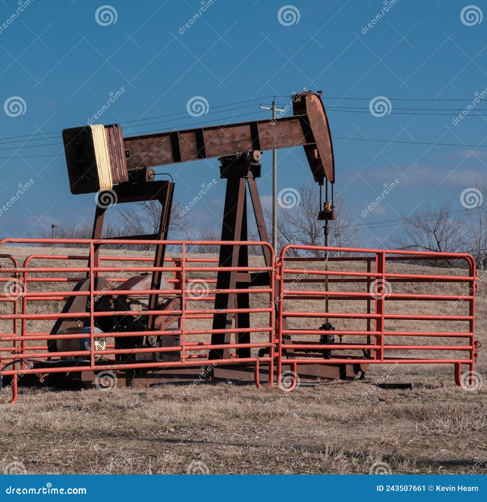 Rusty Oil Well Pumping in Front of Blue Sky with Orange Fencing Stock ...