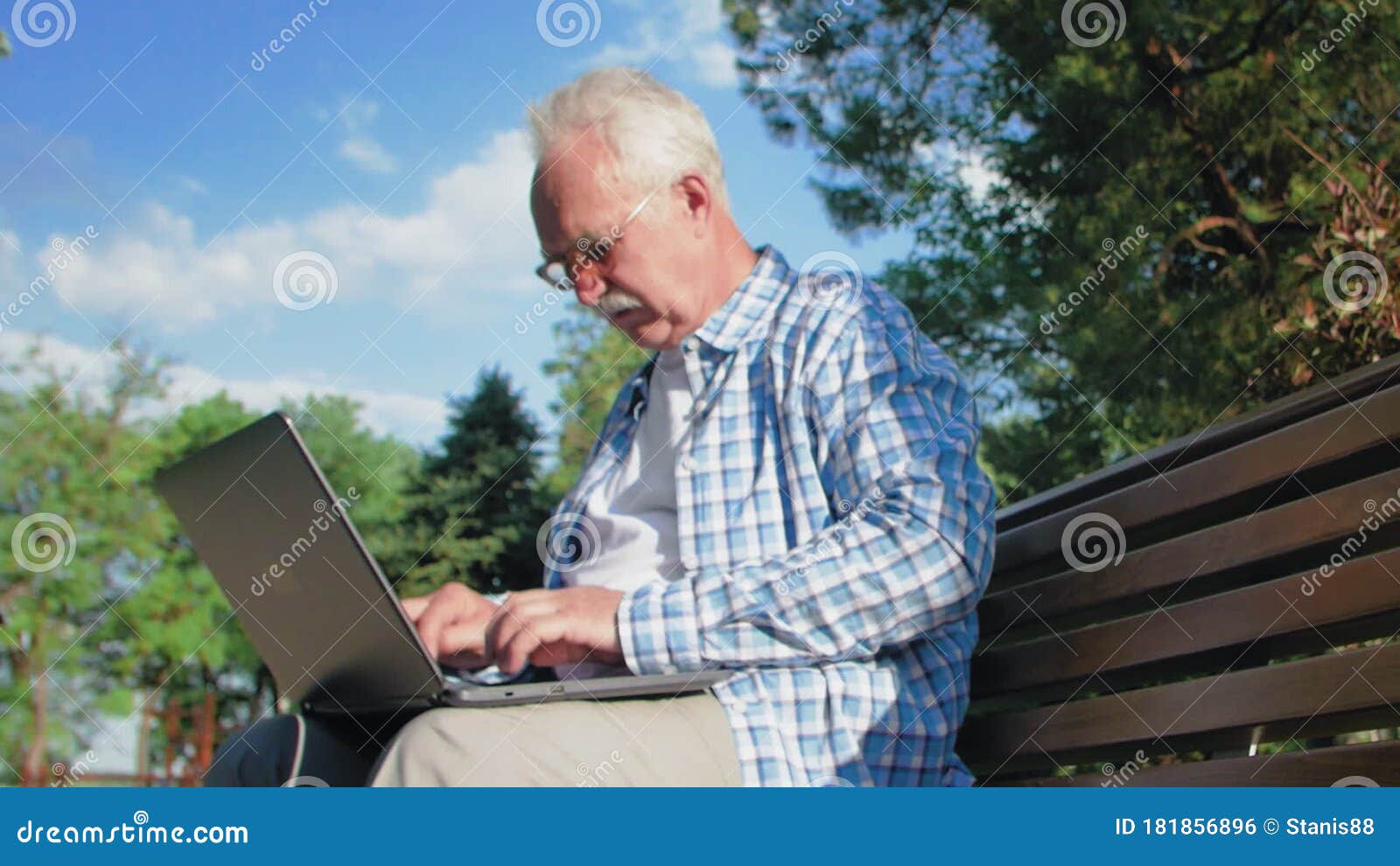 Old Man in Typing Message on Computer while Sitting on Bench in the ...