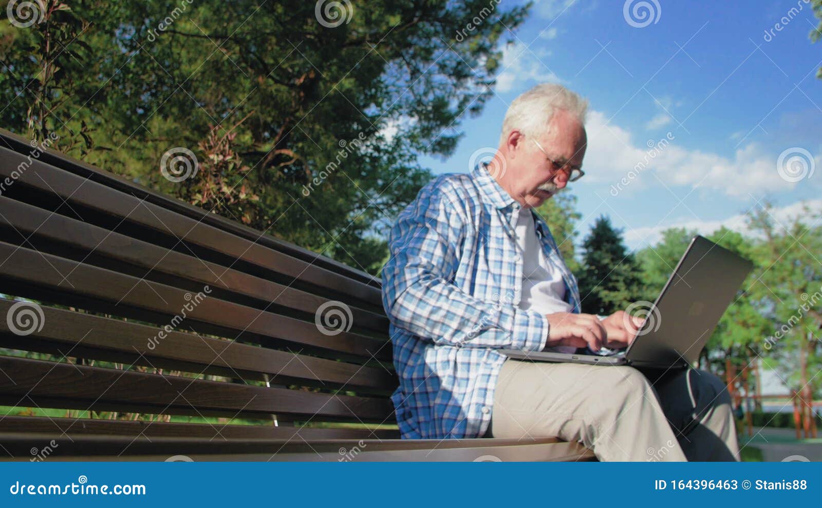 Old Man in Typing Message on Computer while Sitting on Bench in the ...