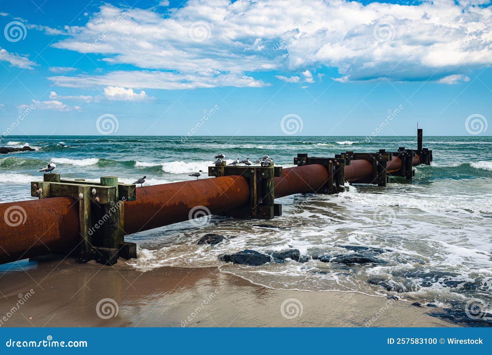 Rusty Water Pipes Over the Sea with Foamy Waves Under a Blue Cloudy Sky ...