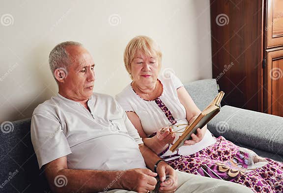 Older Man And Woman 60 65 Years Old Sitting On The Sofa And Read Stock
