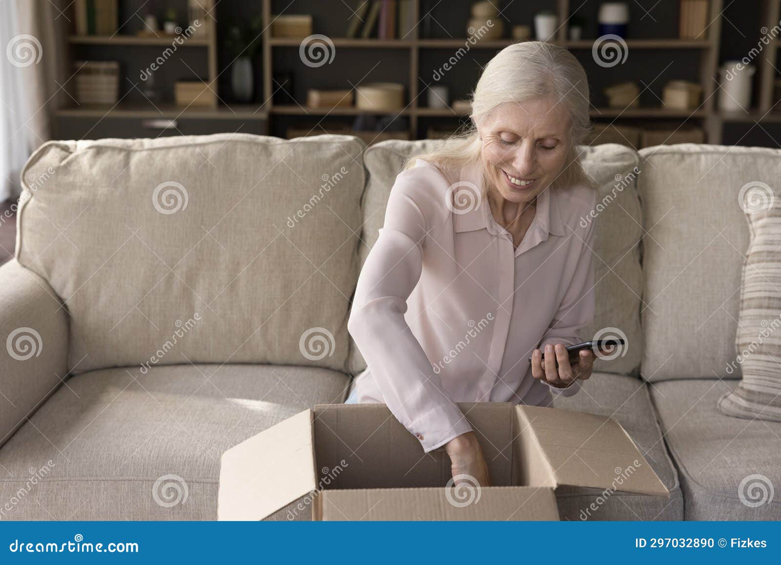 Older Woman Unpacking Received Parcel Box, Holds Cellphone Stock Photo ...