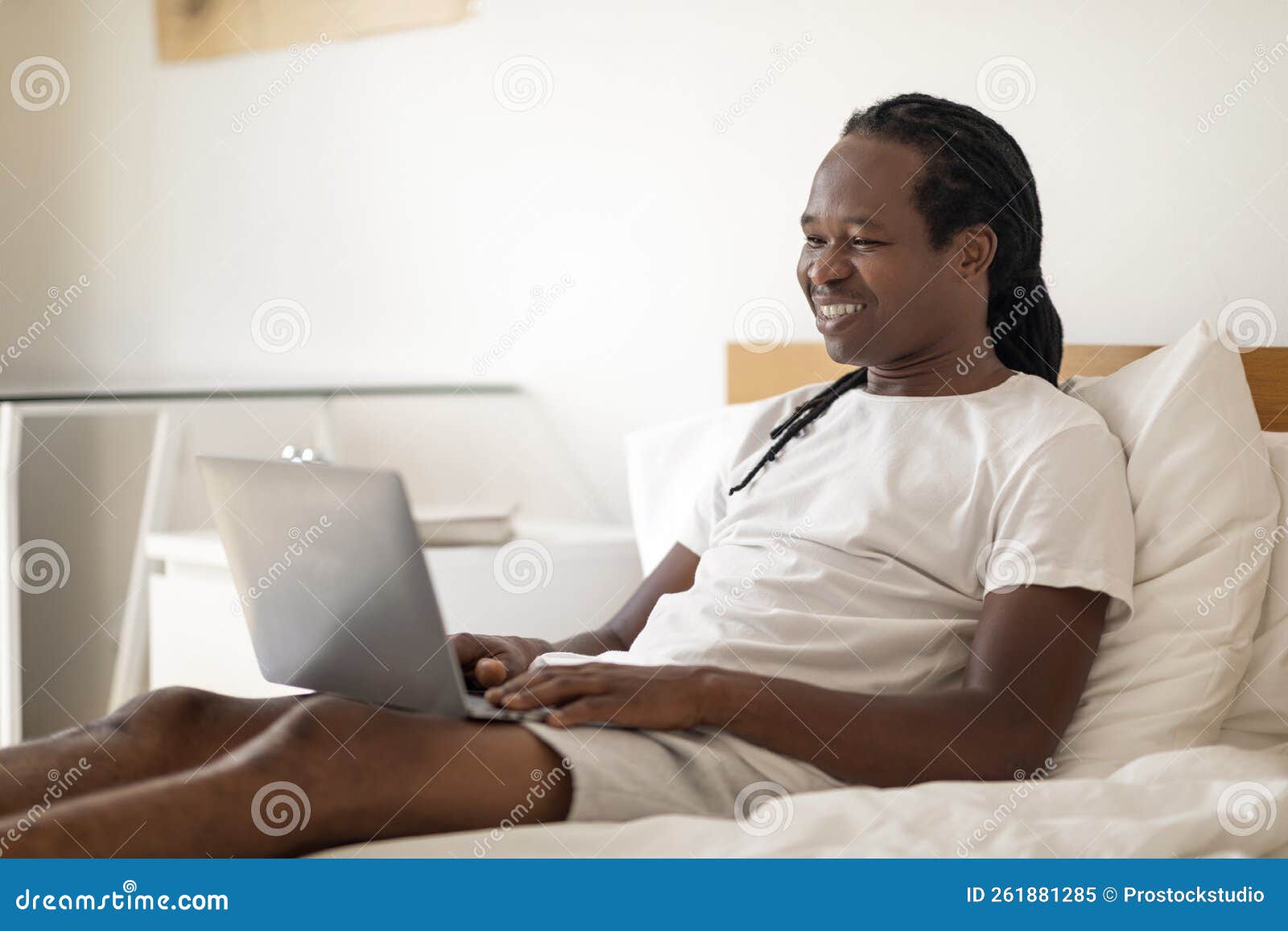 Online Work. Smiling Young Black Man Using Laptop while Sitting in Bed ... Online Work. Smiling Young Black Man Using Laptop while Sitting in Bed ...