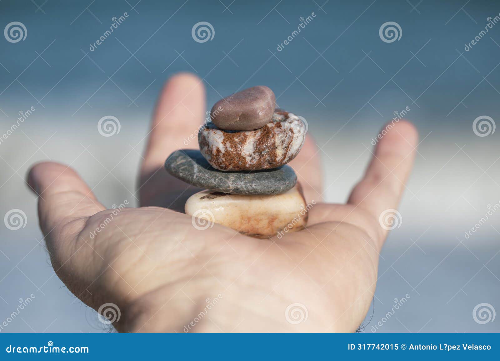 Open Hand with a Stack of Four Pebbles of Different Colors on a Beach ...