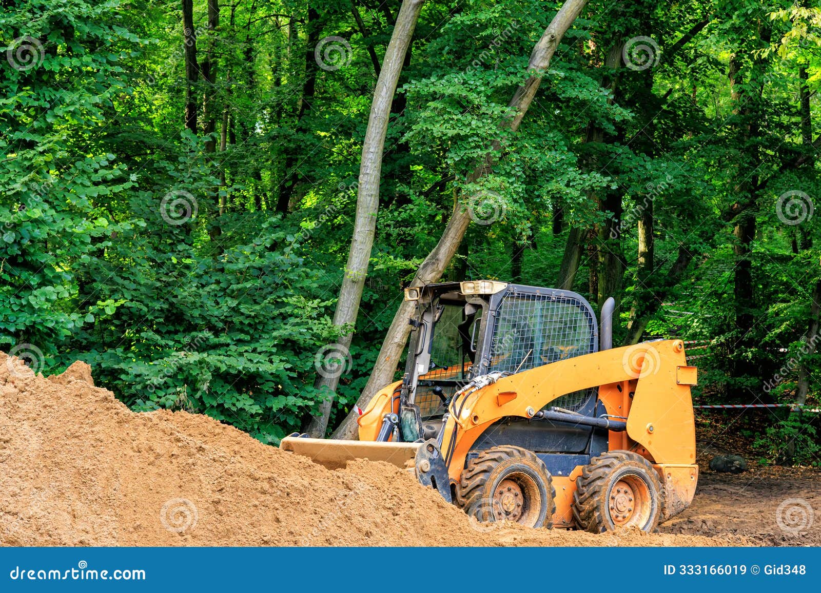 A Skid Steer Loader Shovels Soil Against a Backdrop of Trees Stock ...