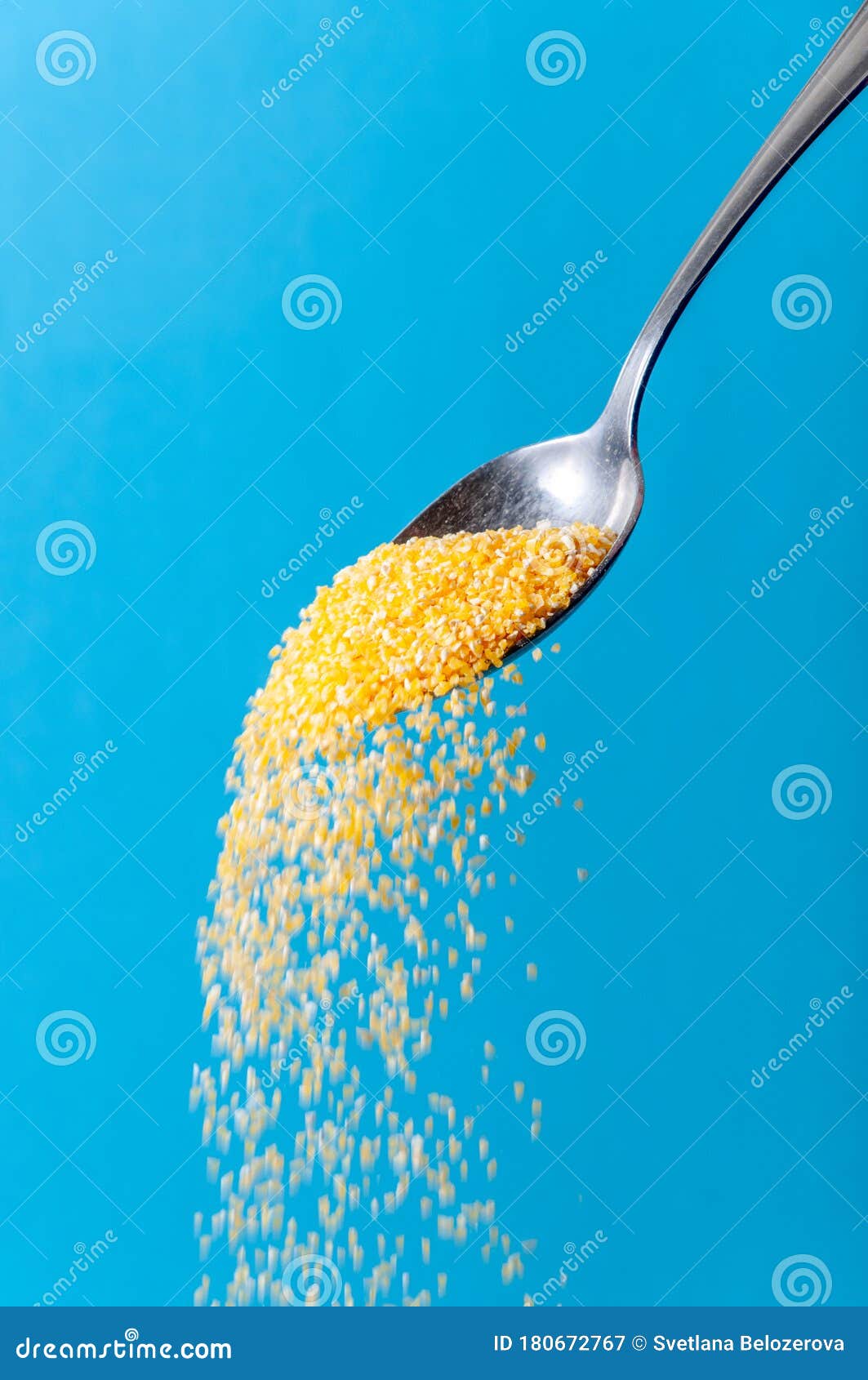 Organic Cereal Grains. Raw Corn Grits Falling from the Spoon on Blue ...