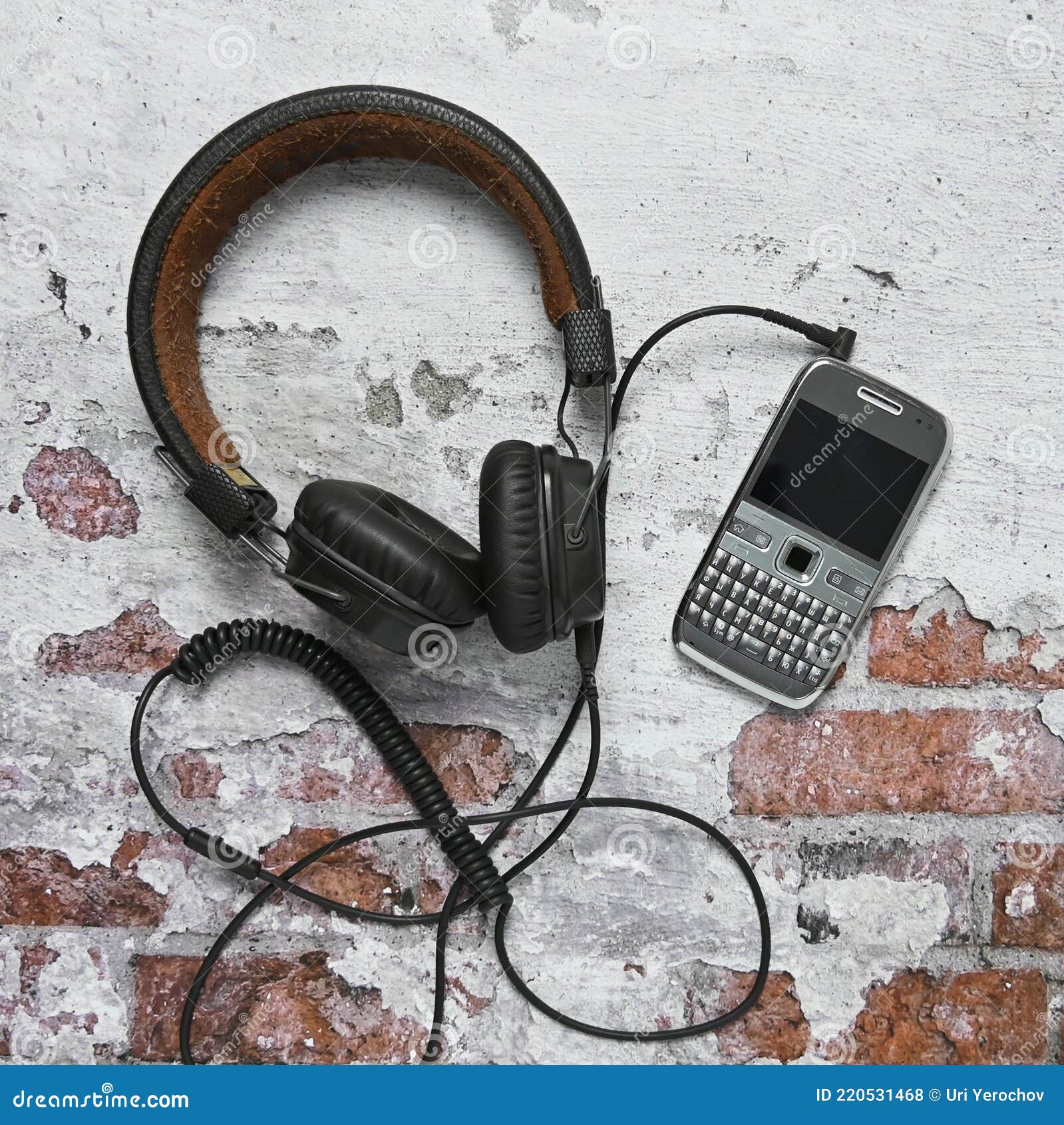 Over-ear Headphones with an Old Push-button Phone Lying on a Brick Wall ...
