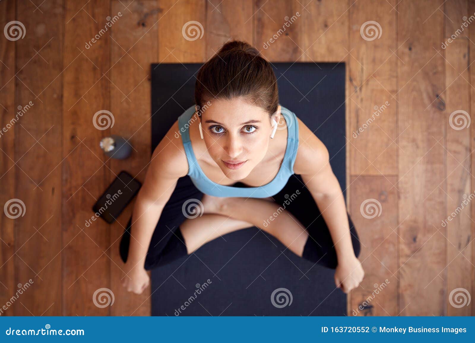 Overhead Portrait Of Woman Sitting On Exercise Mat Wearing Wireless