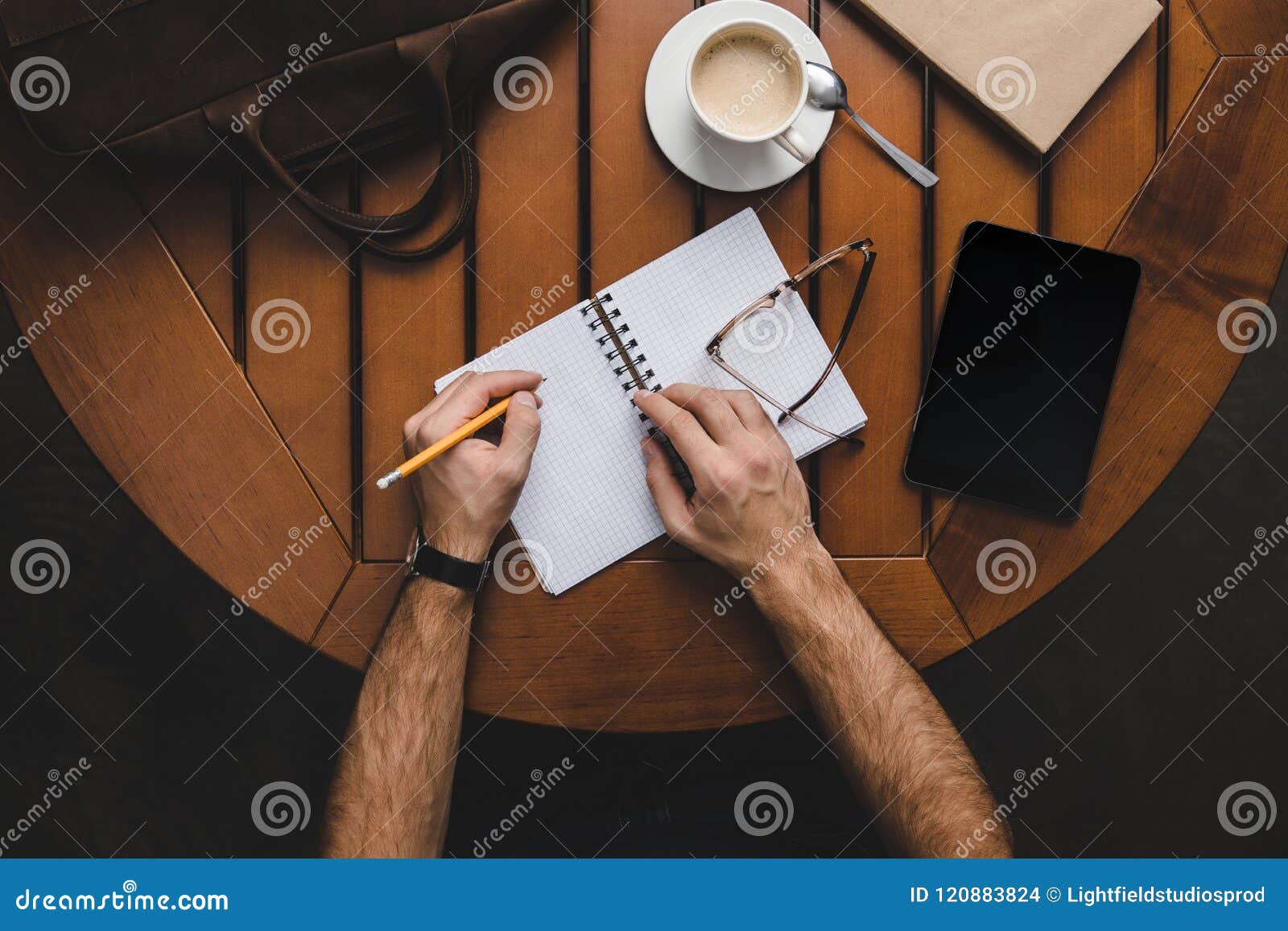 Overhead View of Man Writing in Notepad at Wooden Table with Digital ...