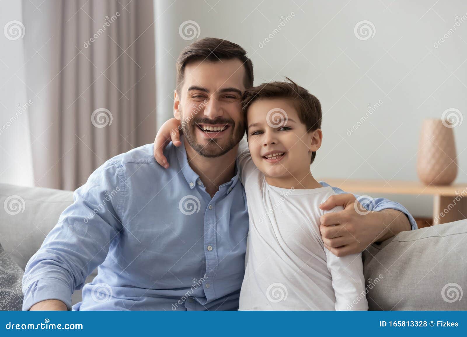 Pai Abraçando A Família Do Filho Sentado No Sofá Olhando A Câmera Foto