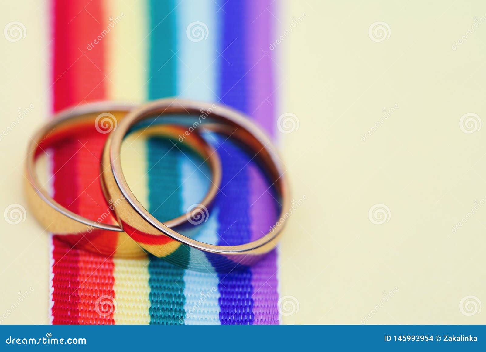 Pair Of Golden Wedding Rings On Lgbt Rainbow Ribbon On Yellow Stock