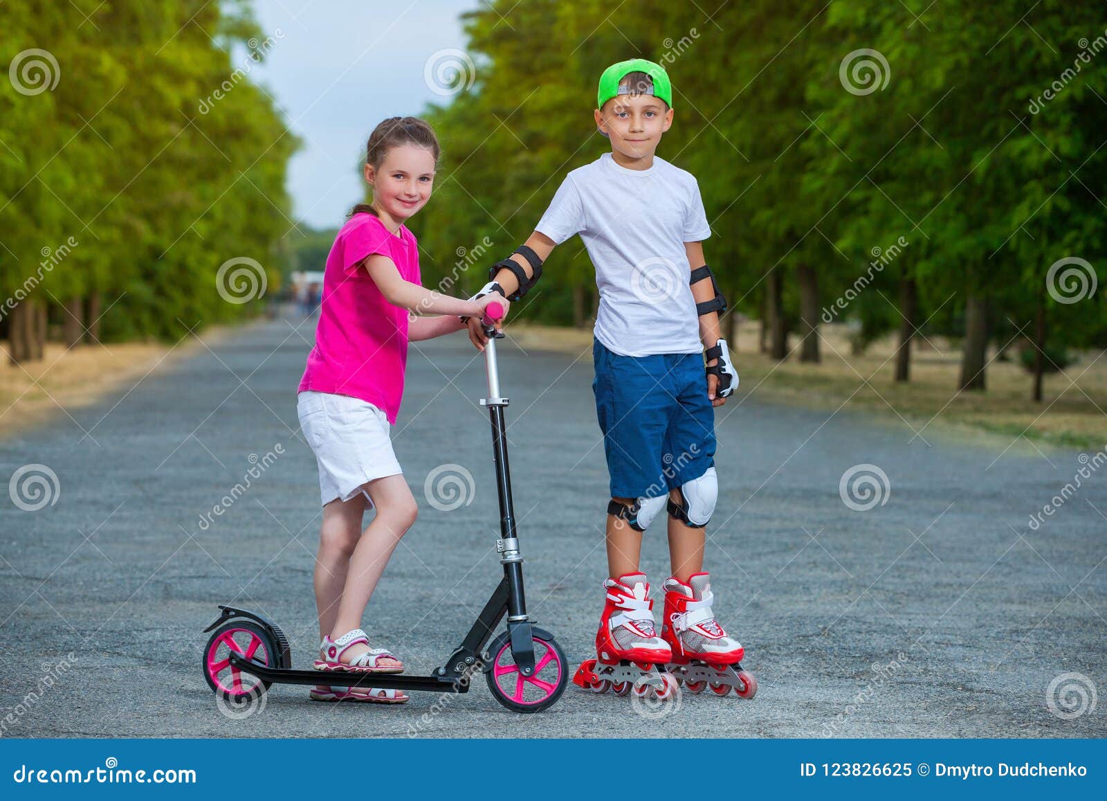 In the Park the Boy Rolls on Rollers and the Girl Rolls on a Scooter ...