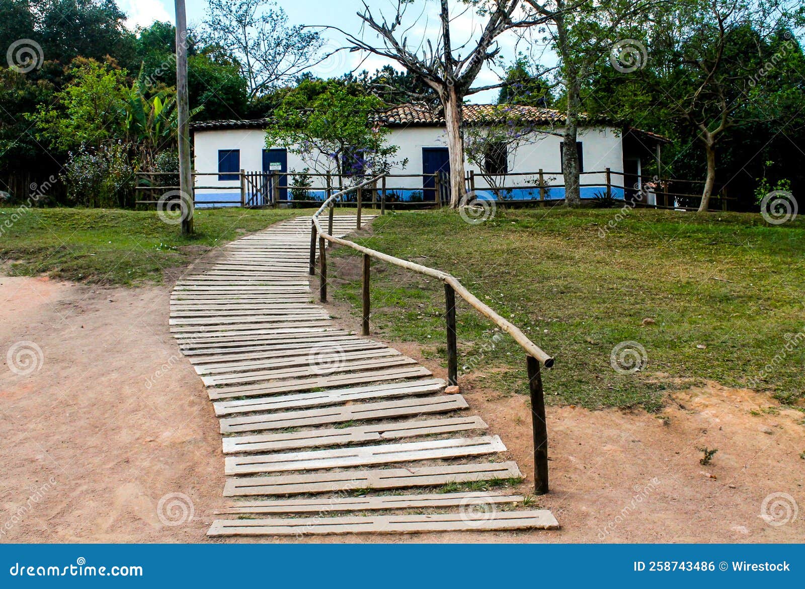 Path with a Wooden Railing and a Rustic White House with Trees in the ...