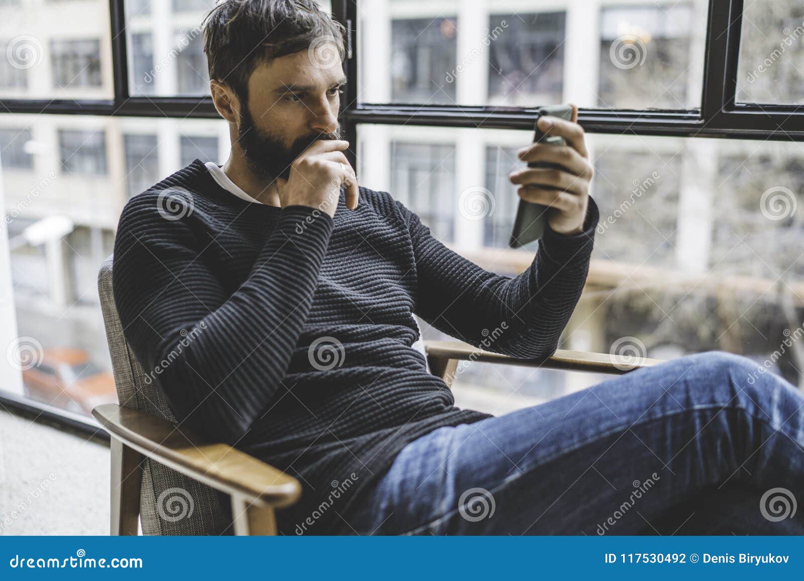 Pensive Adult Bearded Man Sitting At Home And Holding Hands Mobile