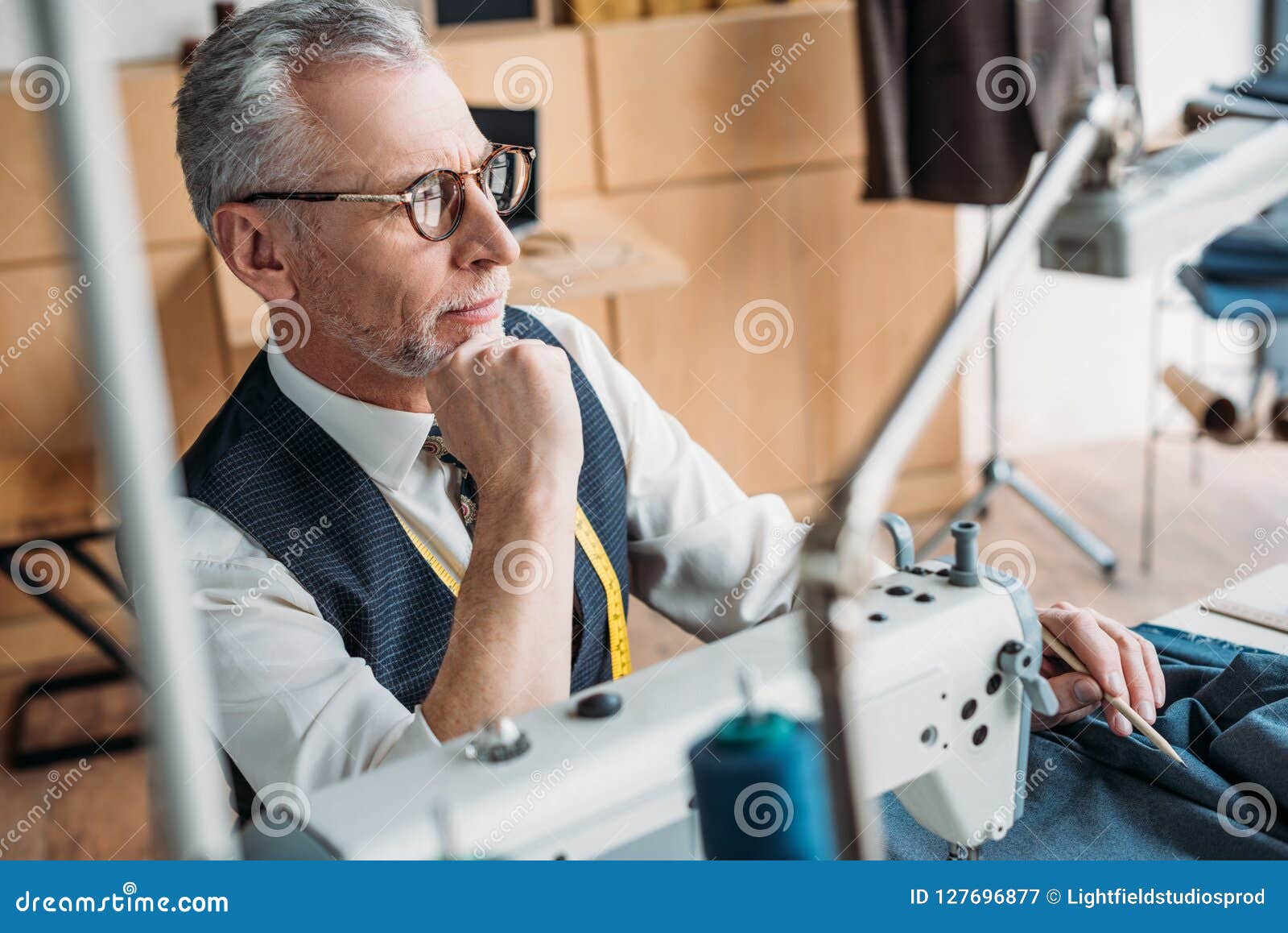 Pensive Tailor Sitting at Table with Sewing Machine and Looking Away ...