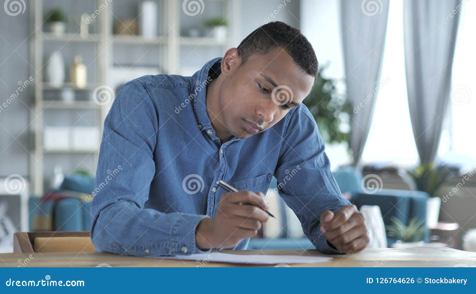 Pensive Young African Man Reading and Writing on Documents, Paperwork ...