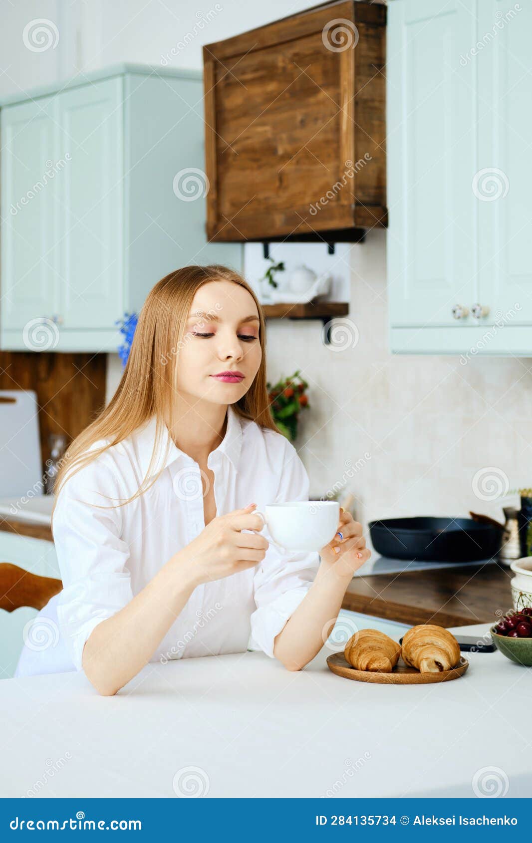 Pensive Young Woman Sits Behind the Kitchen Table with Cup of Coffee ...