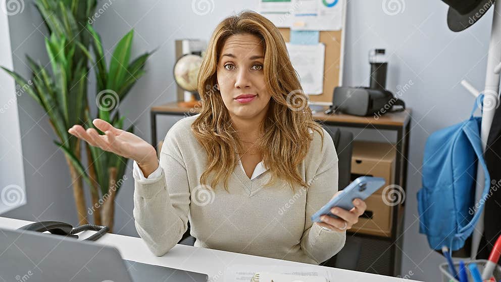 A Perplexed Young Hispanic Woman with a Smartphone Gestures ...