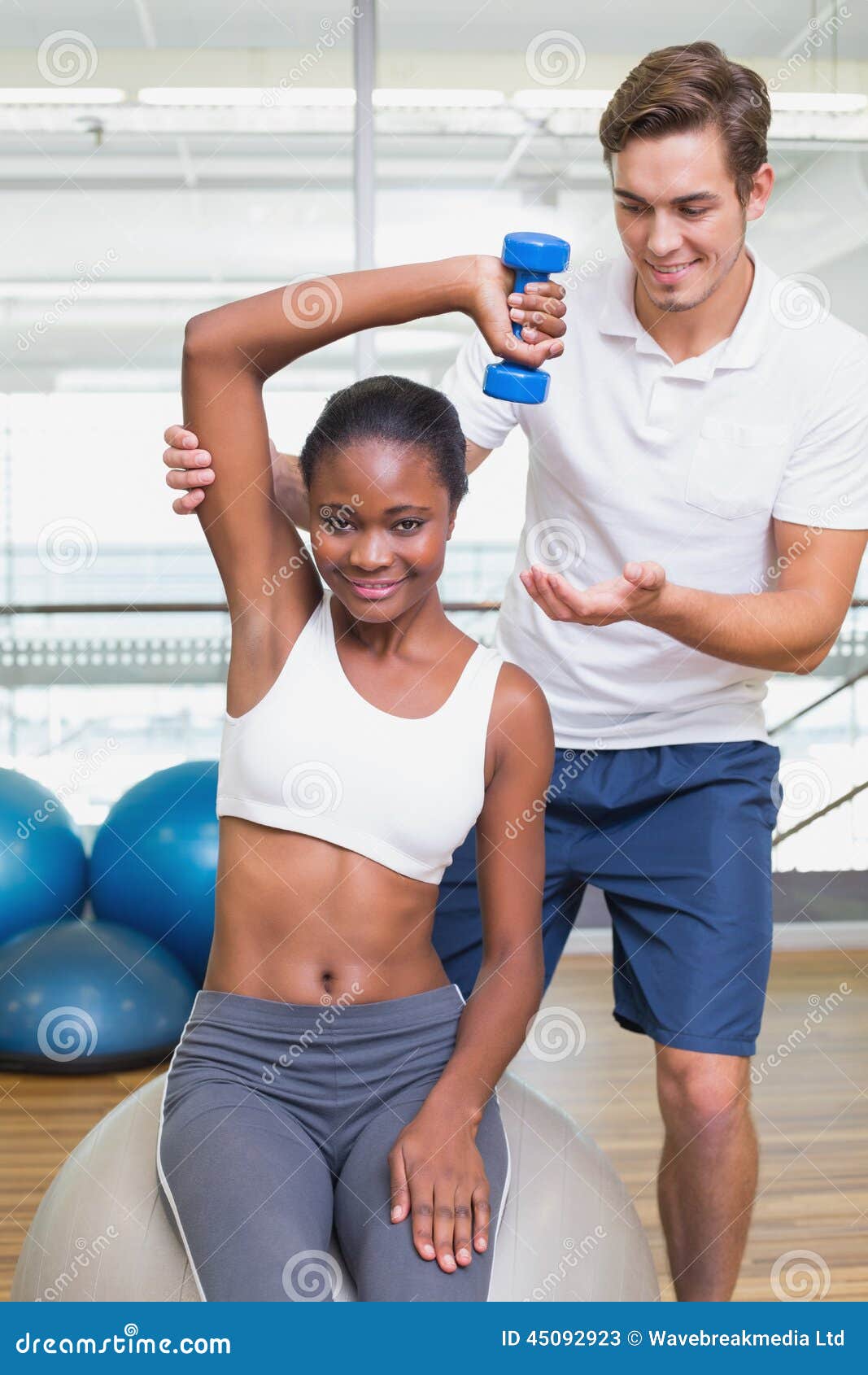Personal Trainer Helping Client Lift Dumbbell on Exercise Ball Stock ...
