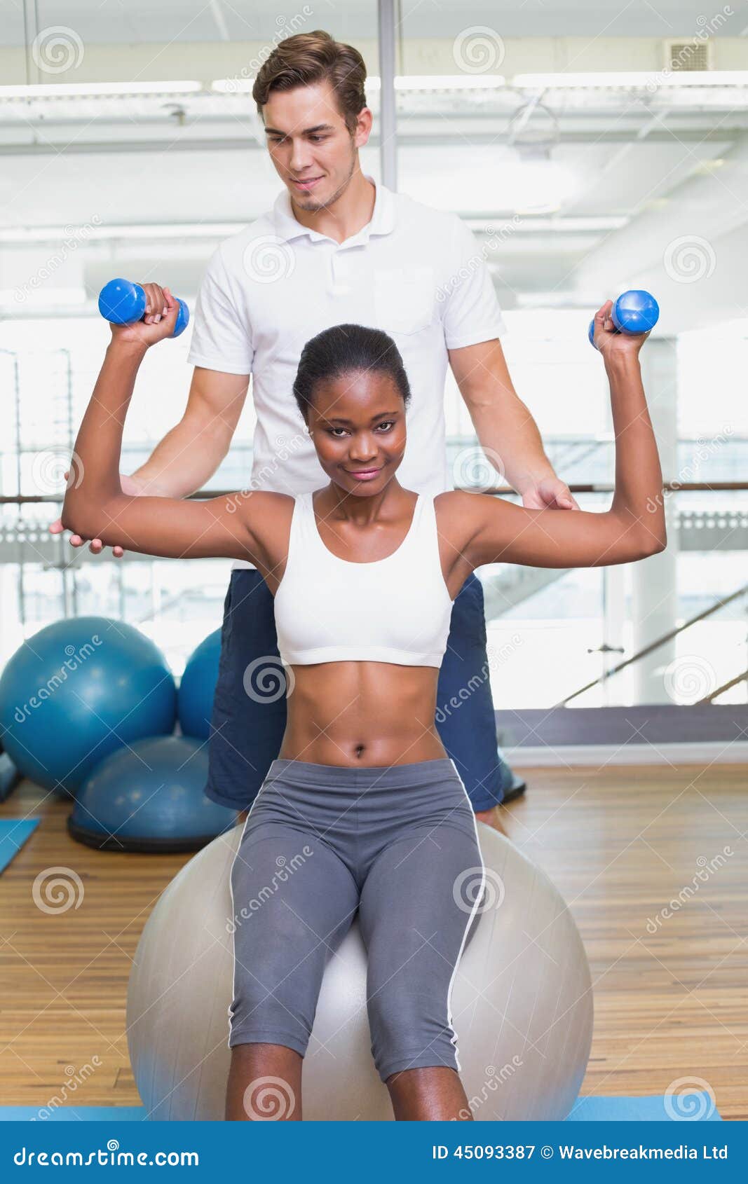 Personal Trainer Helping Client Lift Dumbbell on Exercise Ball Stock ...