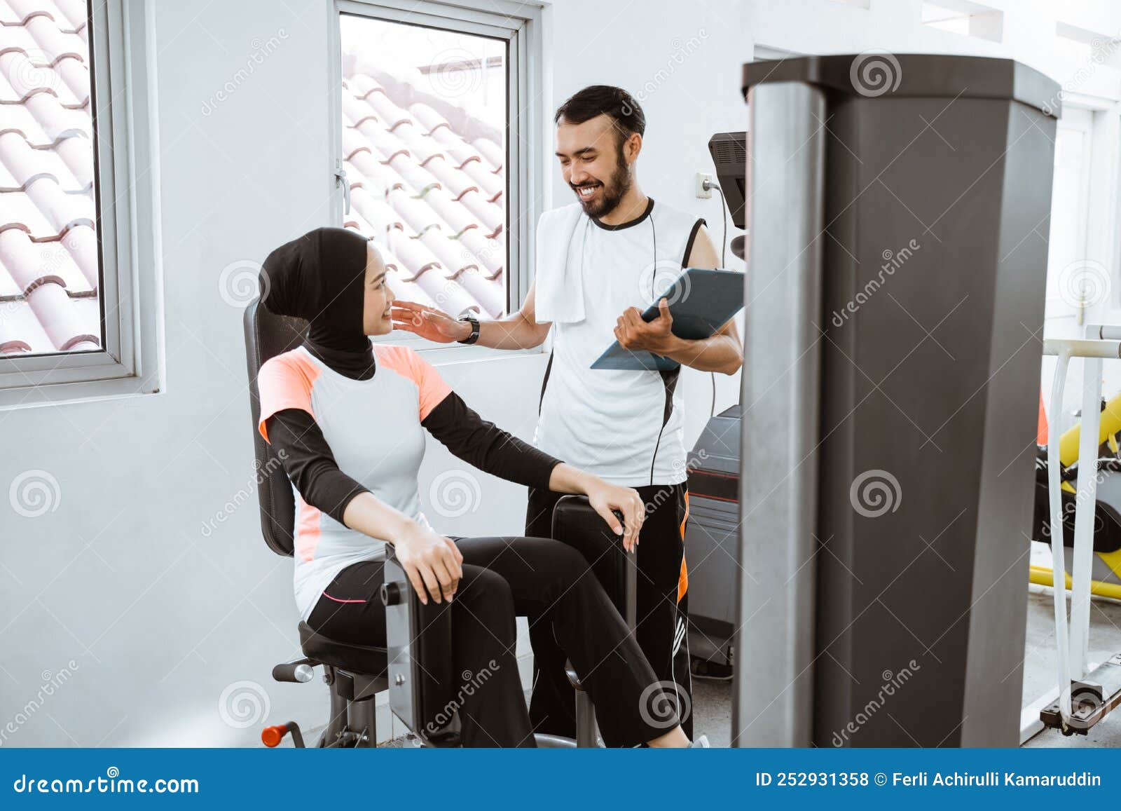 Personal Trainer Helping Woman Working With Leg Weight Machine At The