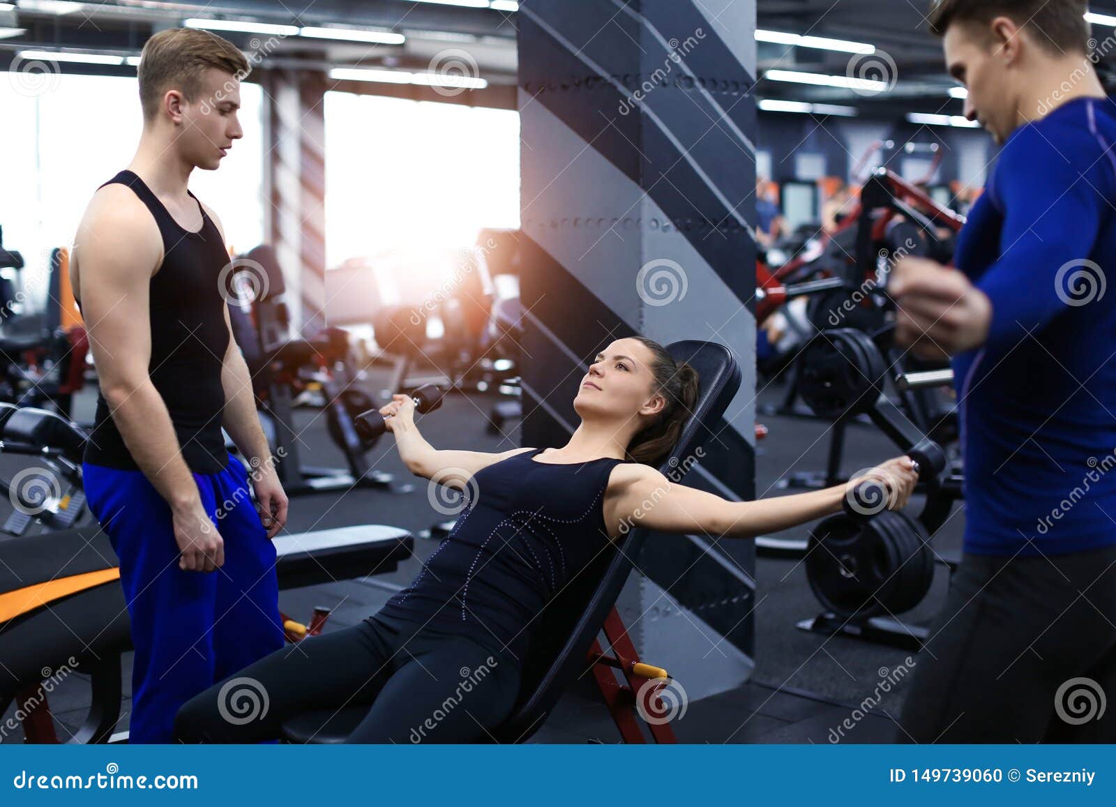 Personal Trainer Helping Young Woman To Do Exercises With Dumbbells In