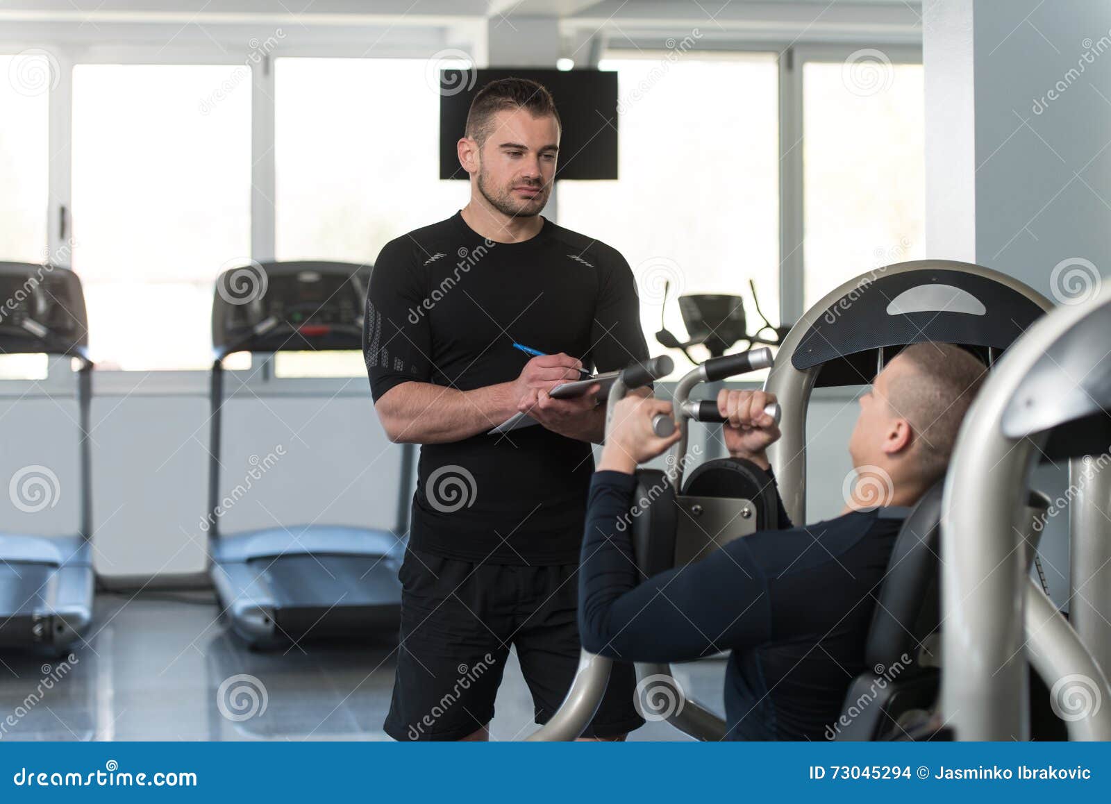 Personal Trainer Takes Notes while Man Exercising Chest Stock Photo ...