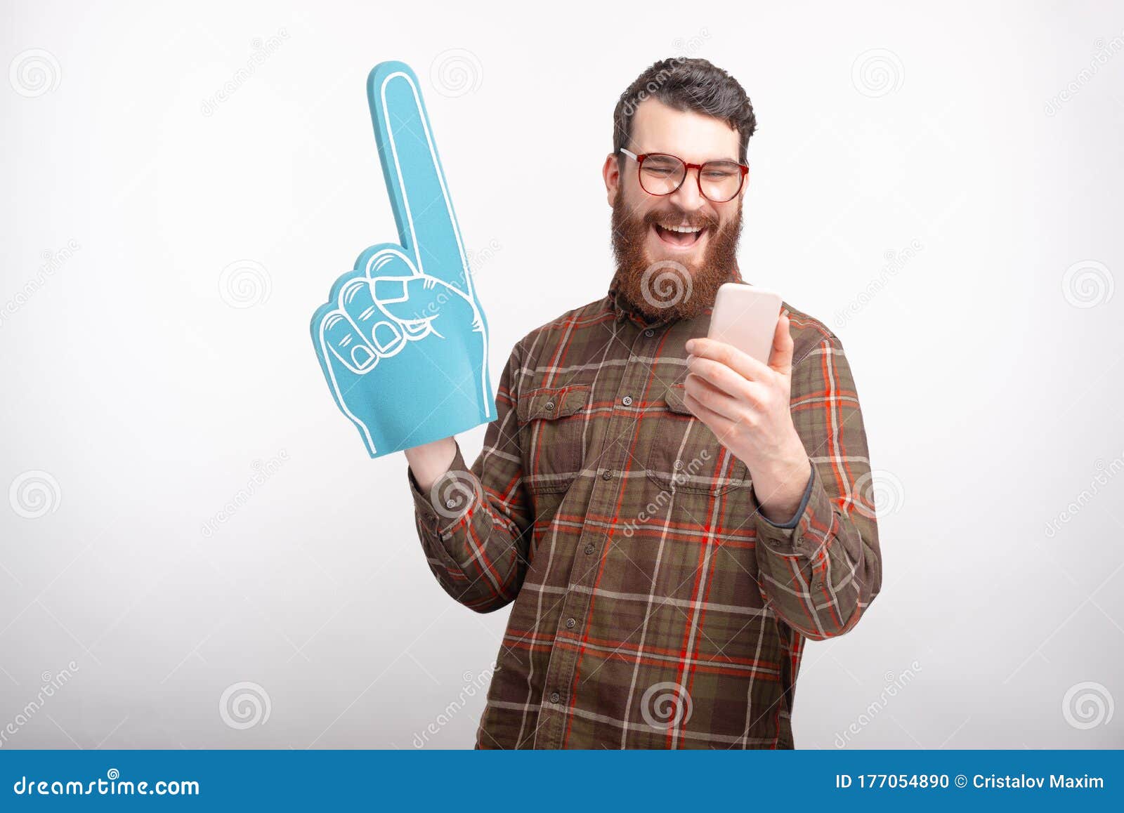Cheerful Smiling Young Man Looking at Smartphone and Holding Fan Foam ... Cheerful Smiling Young Man Looking at Smartphone and Holding Fan Foam ...