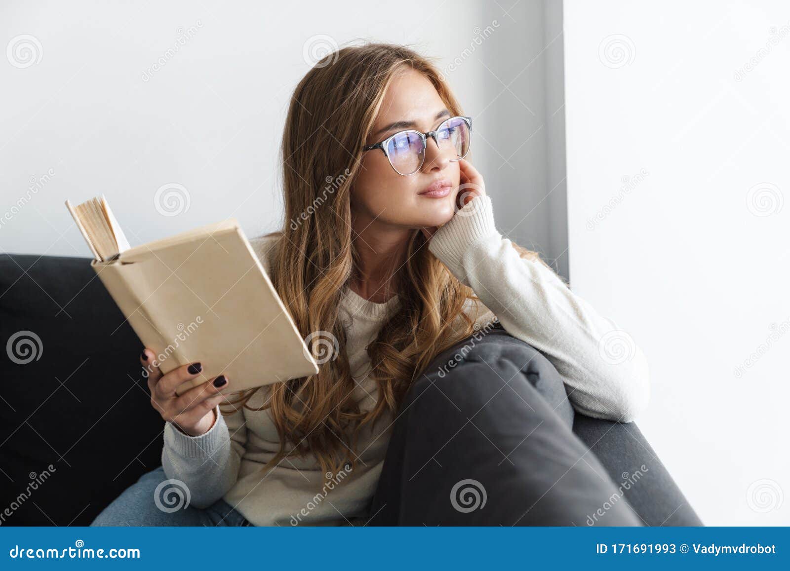 Photo Of Young Serious Woman Reading Book While Sitting On Couch Stock