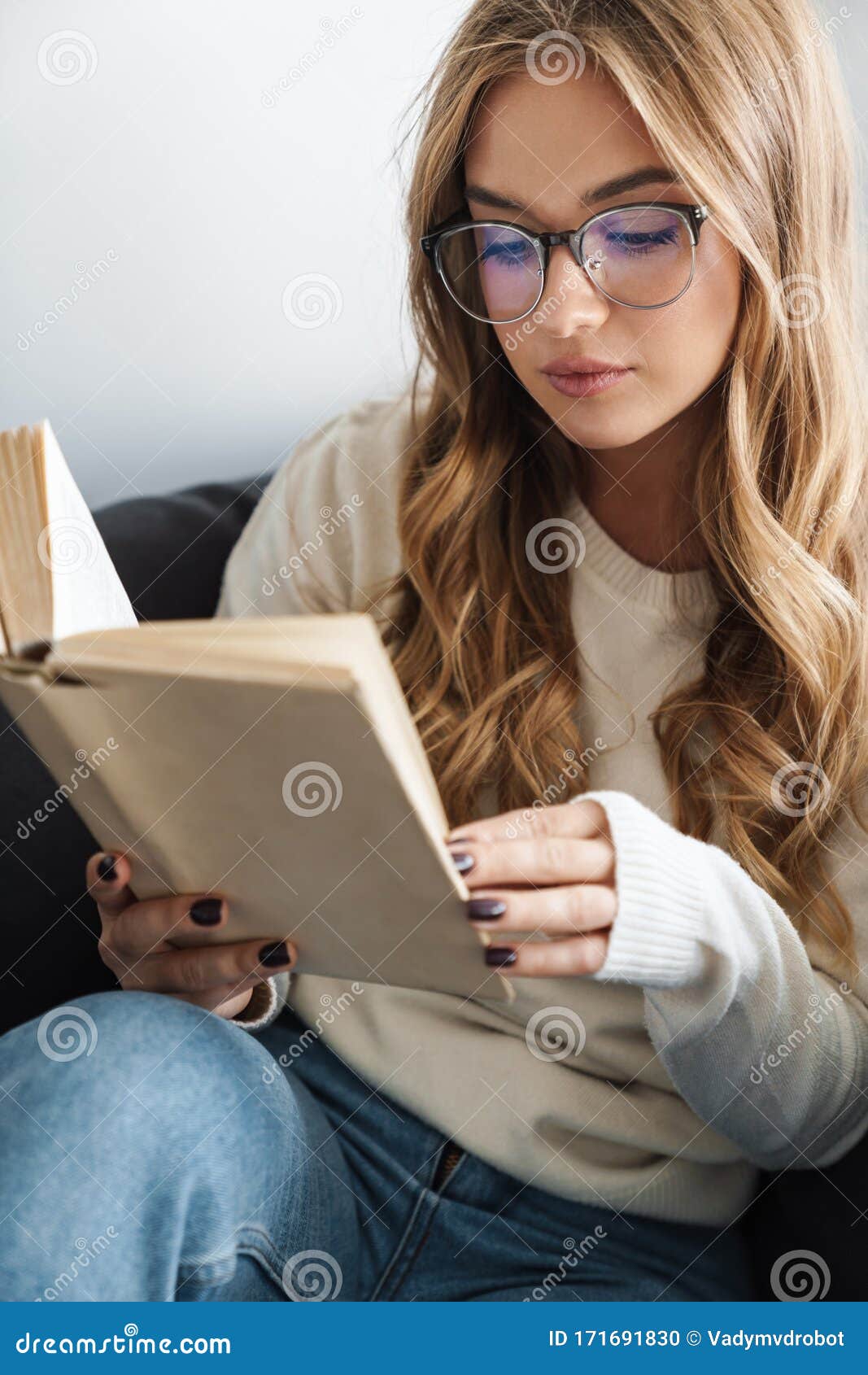 Photo Of Young Serious Woman Reading Book While Sitting On Couch Stock