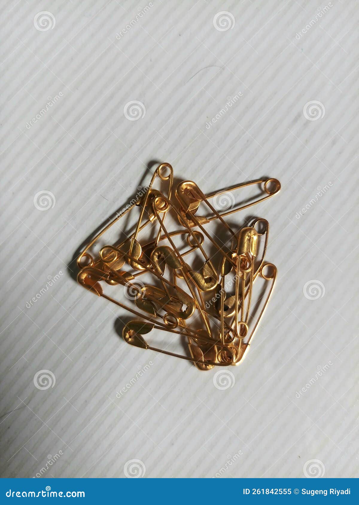 A Pile of Small Gold Safety Pins on White Paper Stock Image - Image of ...