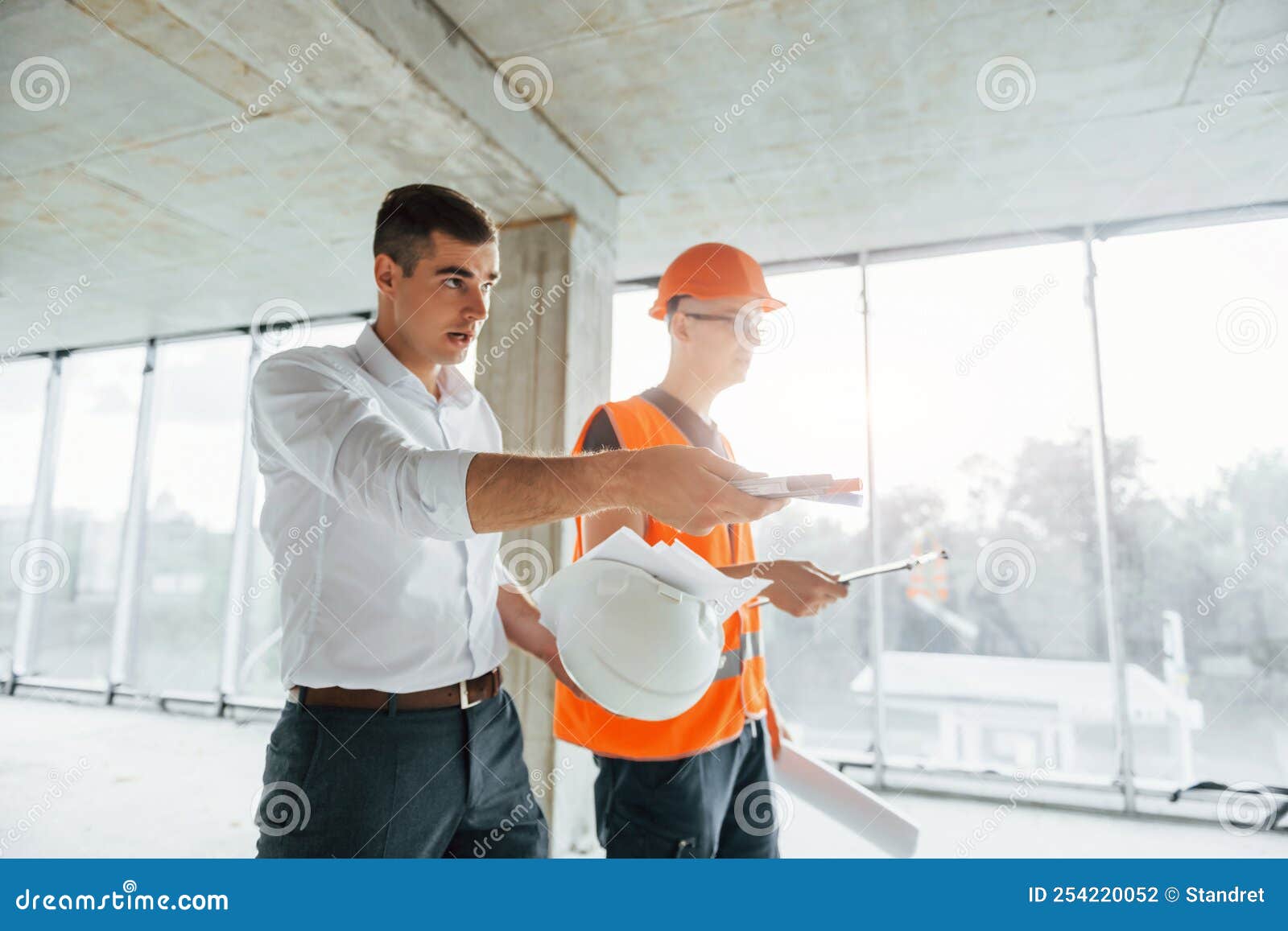 Planning the Process. Man in Suit and Handyman in Orange Protective Wear is Working on ...