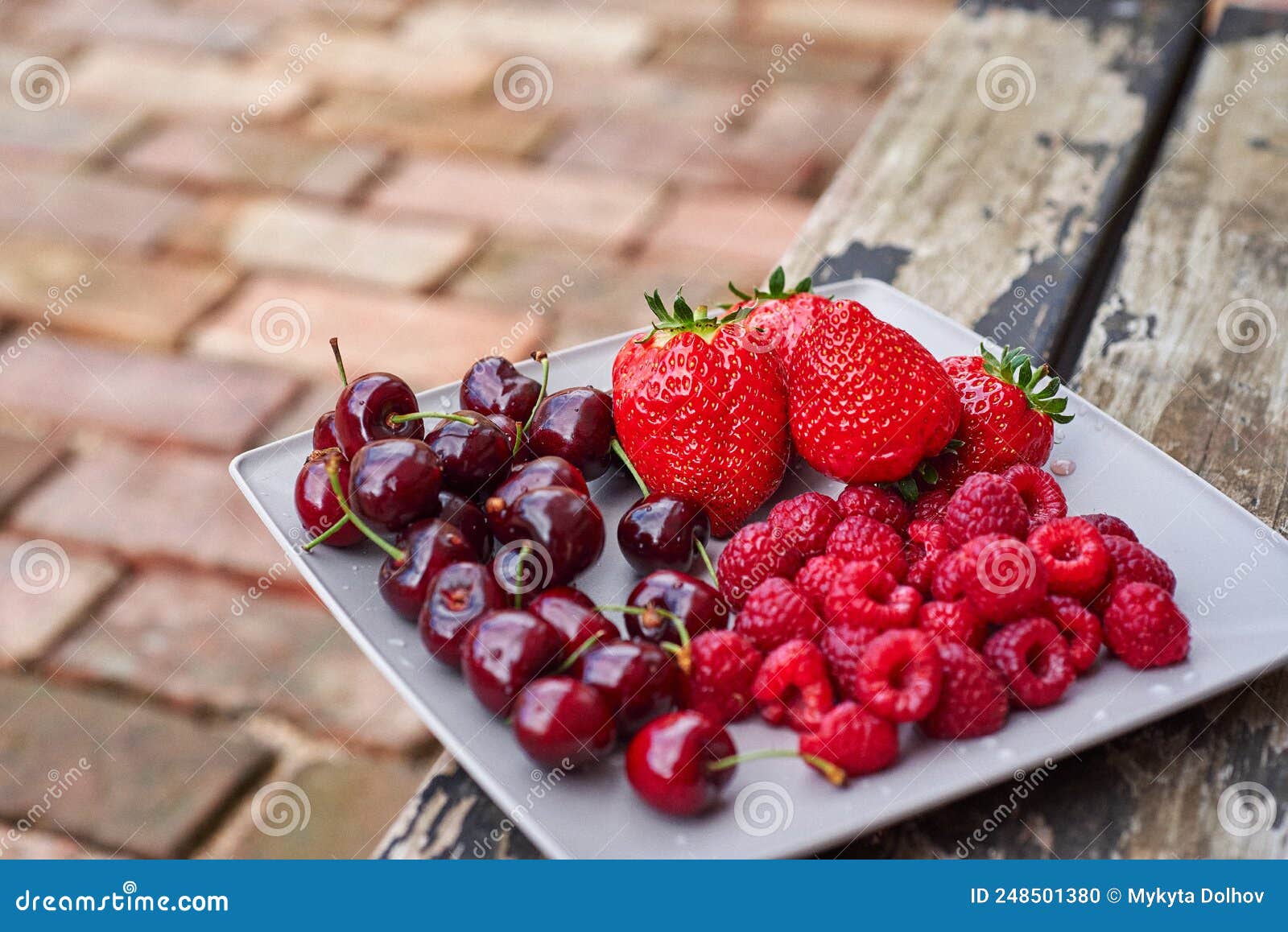 A Plate with Bright Red Fruit Against the Background of a Cracked Bench ...