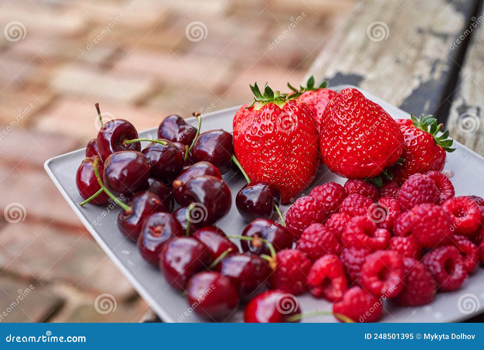 A Plate with Bright Red Fruit Against the Background of a Cracked Bench ...